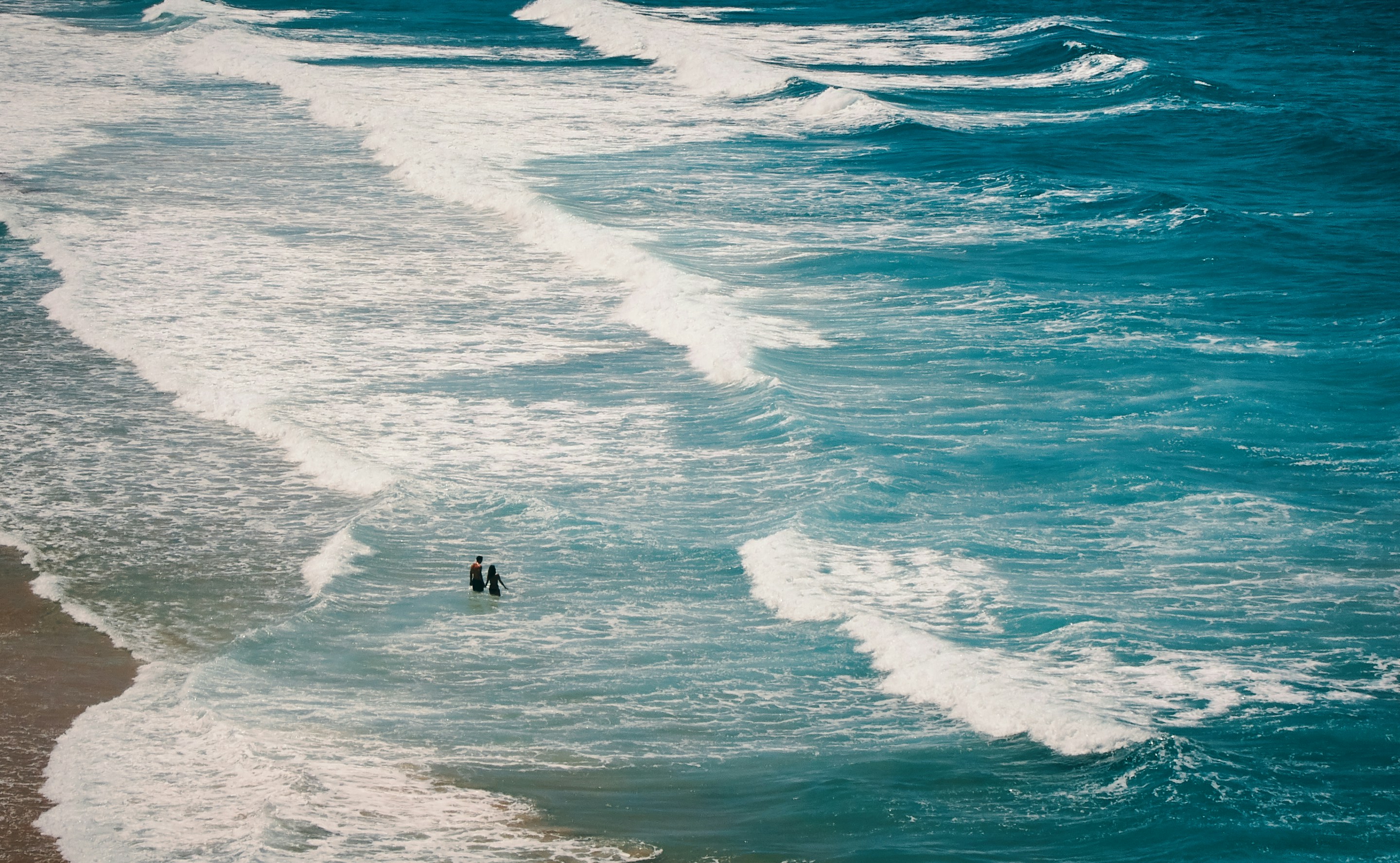 Two people stand together in the shallow waves of a vast ocean.