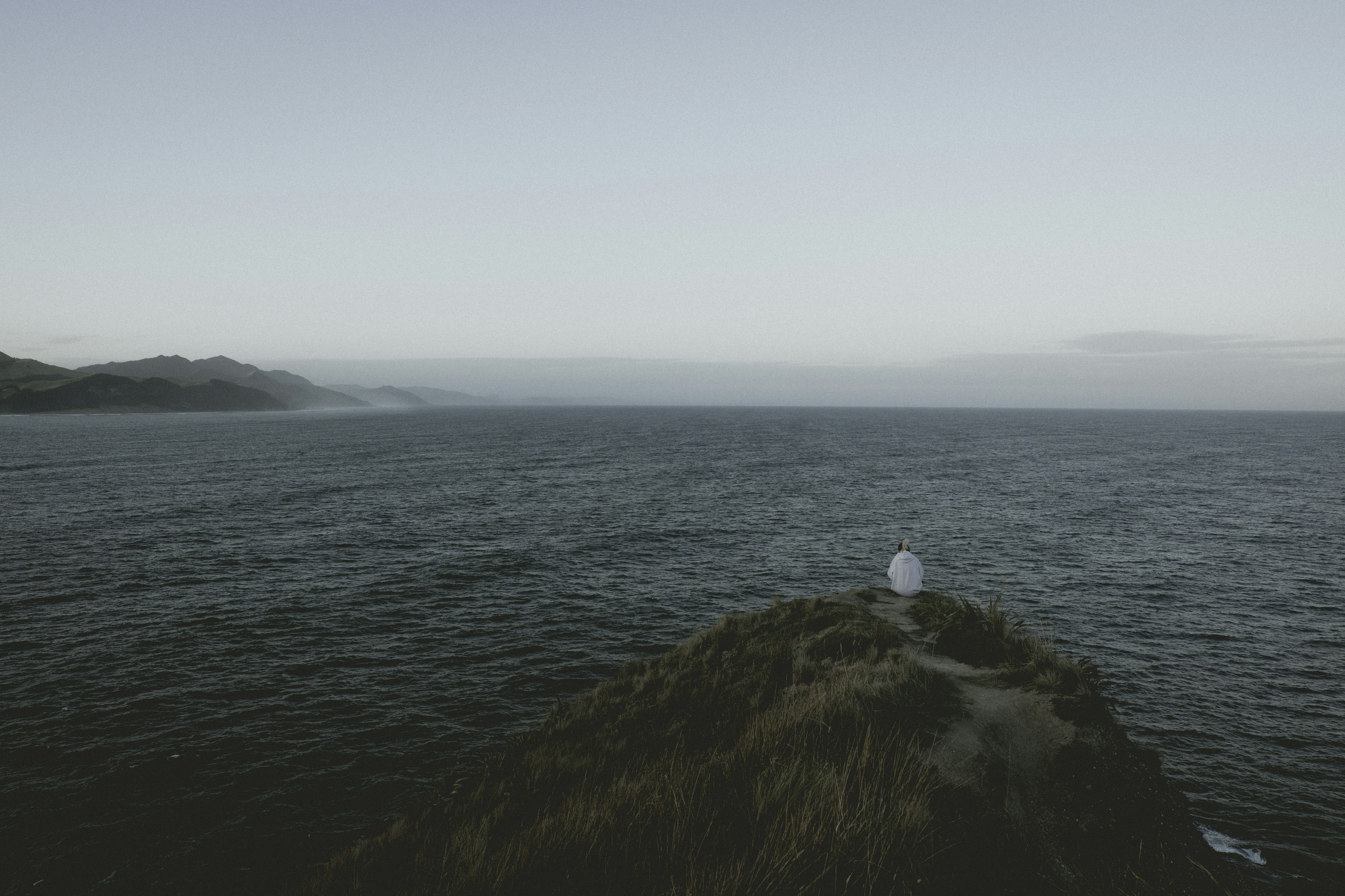 Person standing on a cliff overlooking a vast, calm ocean under a clear sky.