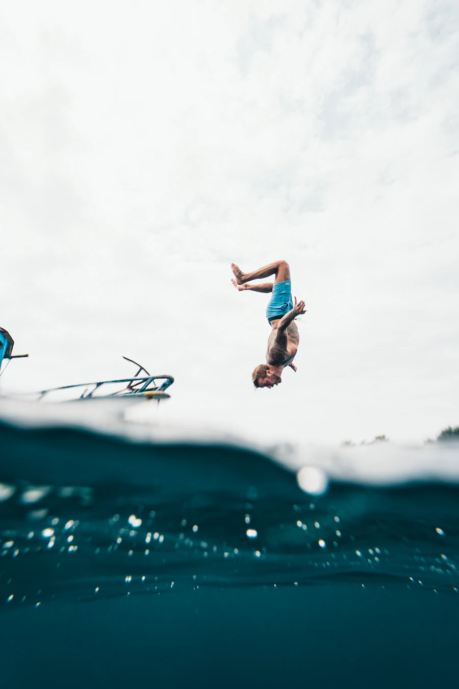 A diver executes a perfect backflip above the water, with a blurred boat in the background. The scene captures the thrill of summer sports.