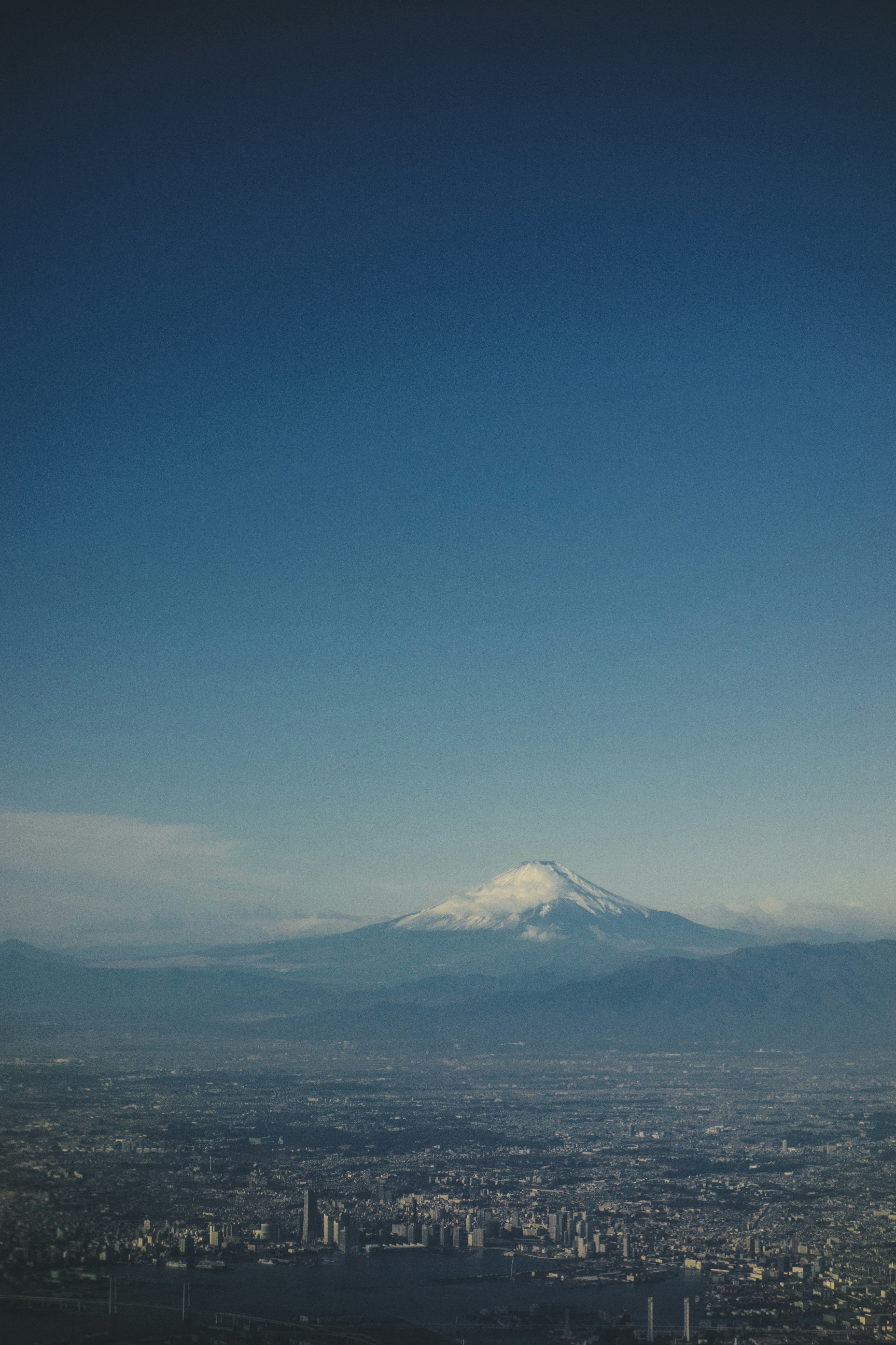 Snow-capped mountain towering over a sprawling cityscape under a clear blue sky.