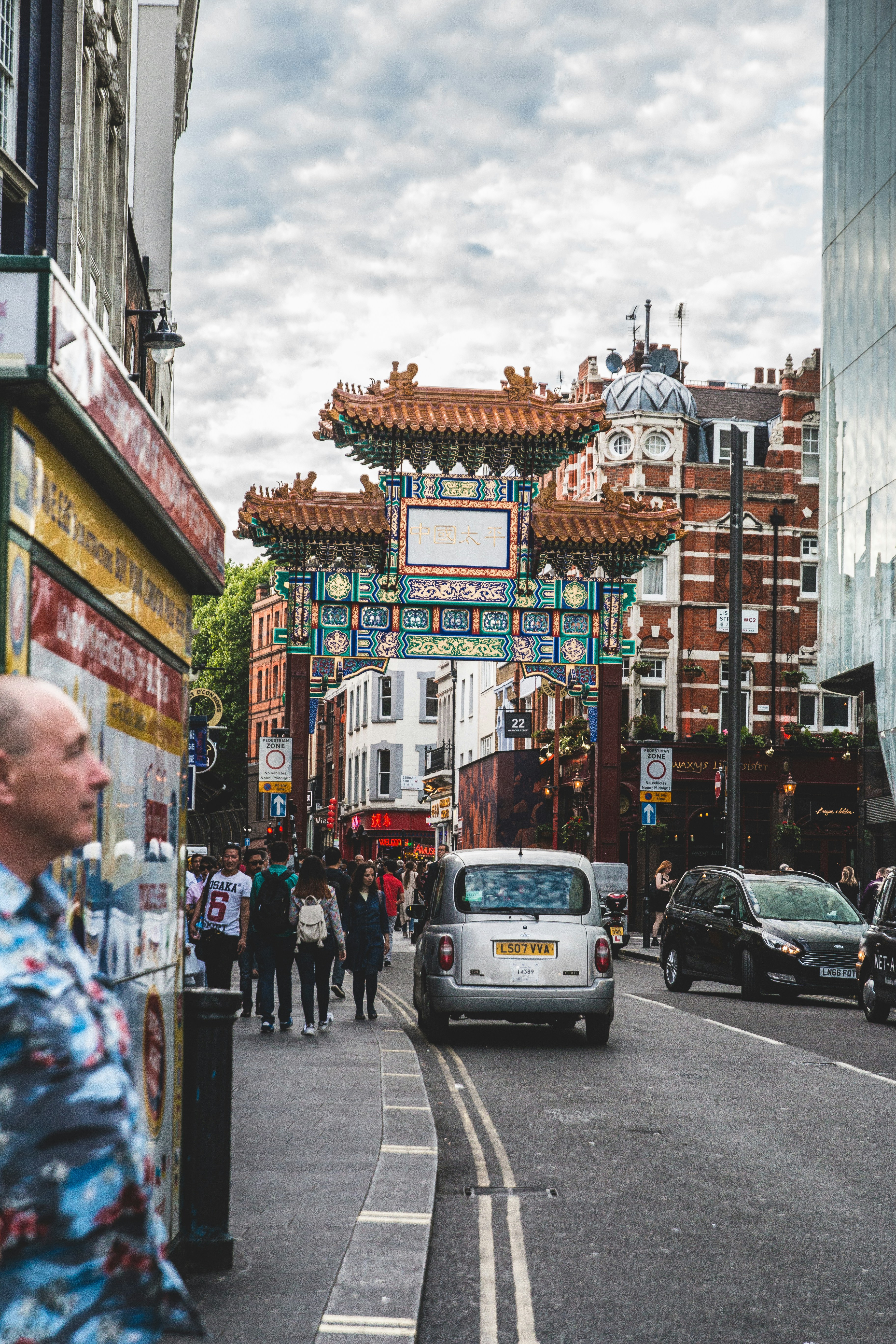 Colorful Chinese archway marking the entrance to a vibrant street filled with pedestrians and vehicles. 