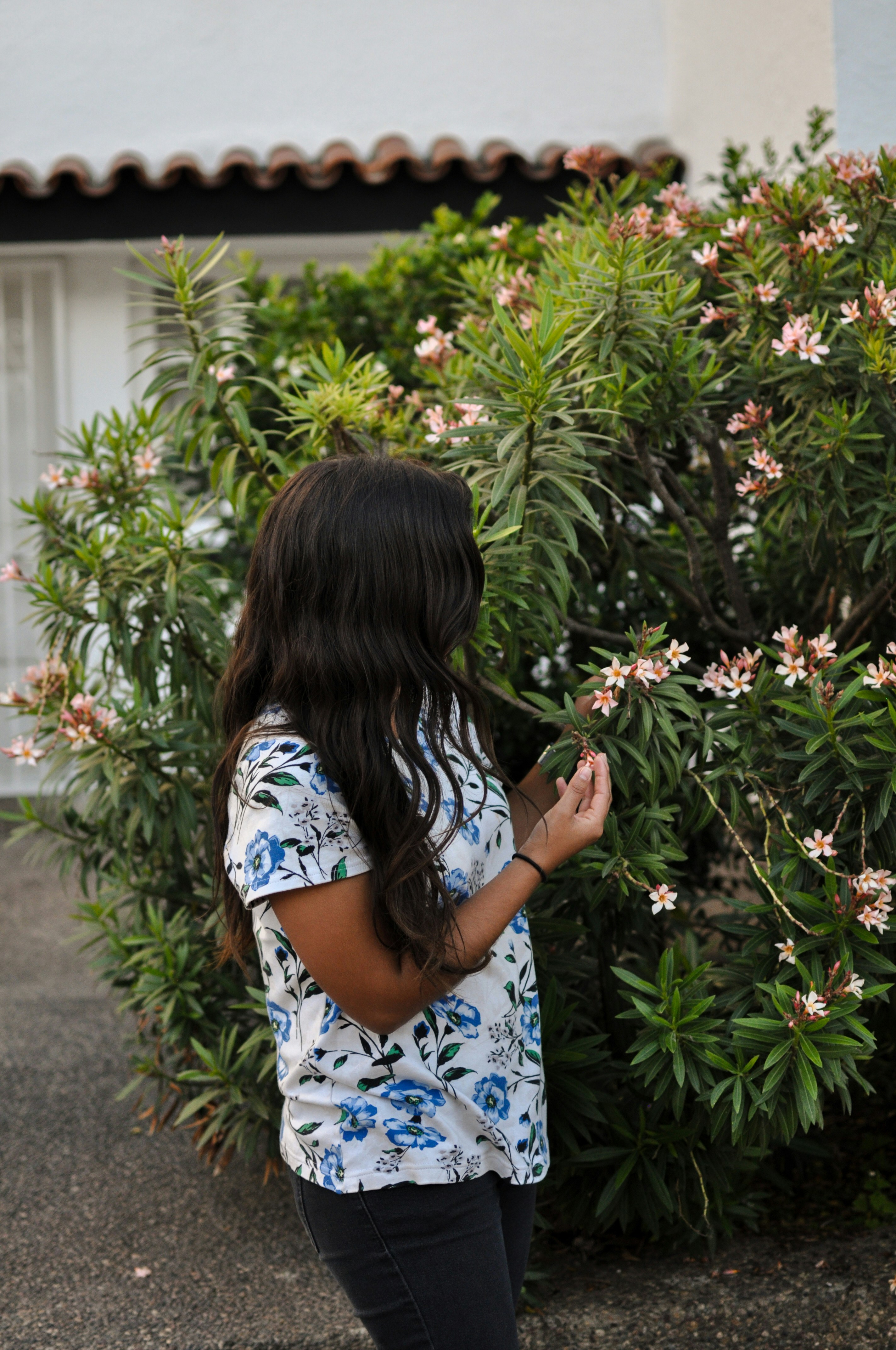 Young girl gently interacting with blooming flowers amidst lush greenery.