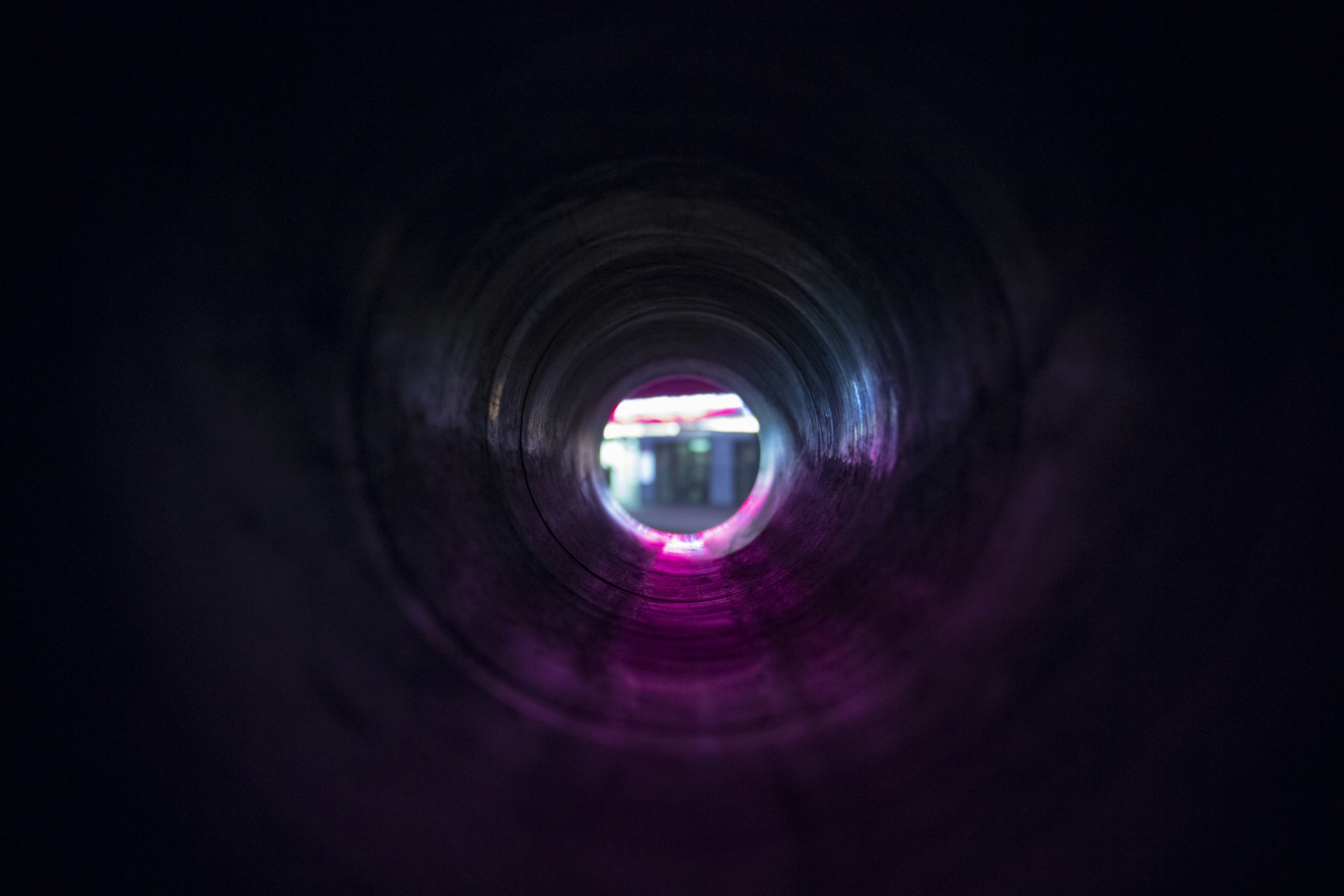 View through a tunnel with vibrant pink and blue neon light illuminating the interior.