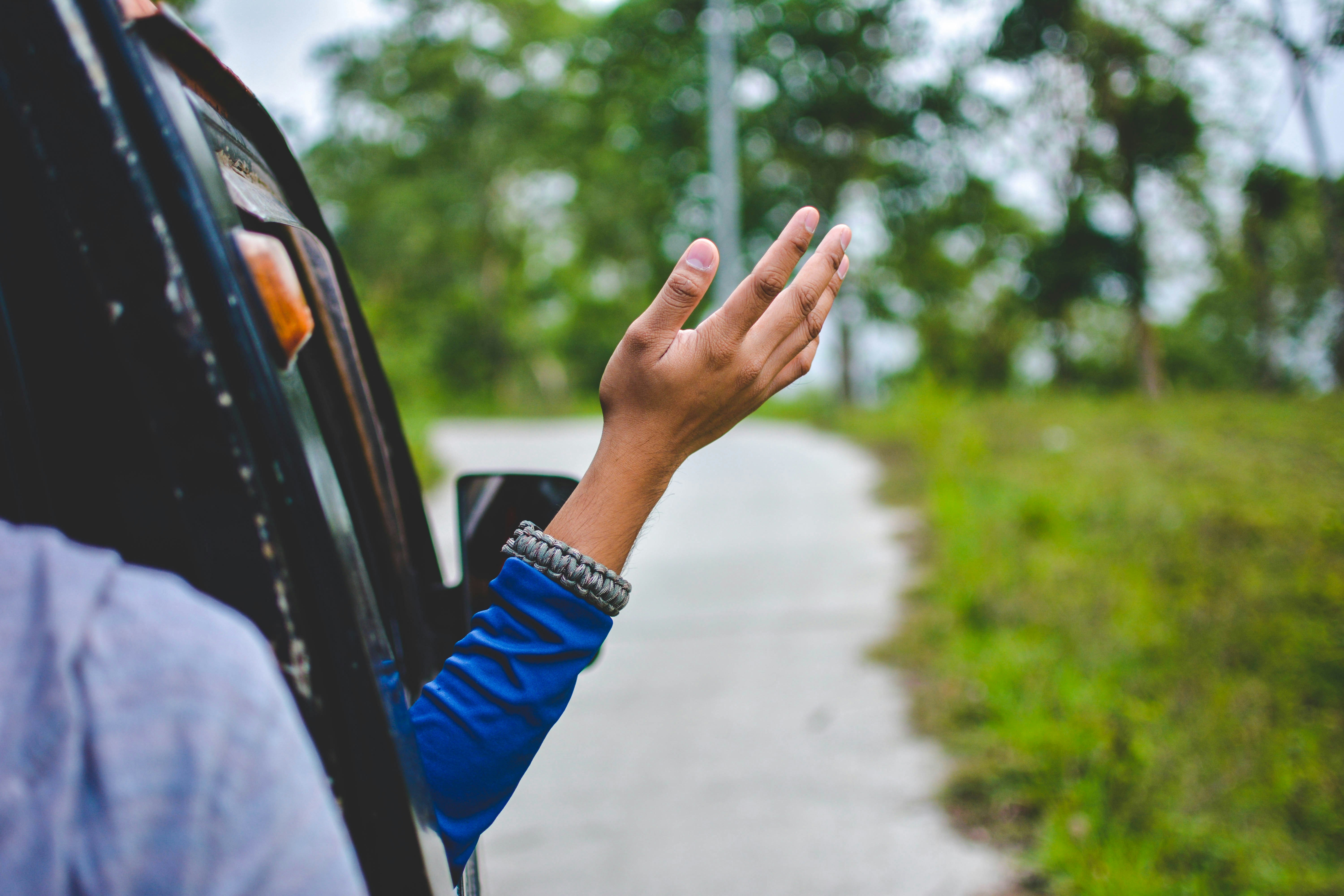 A hand extends from a vehicle window, signaling a moment of spontaneity against a backdrop of greenery and a winding road.
