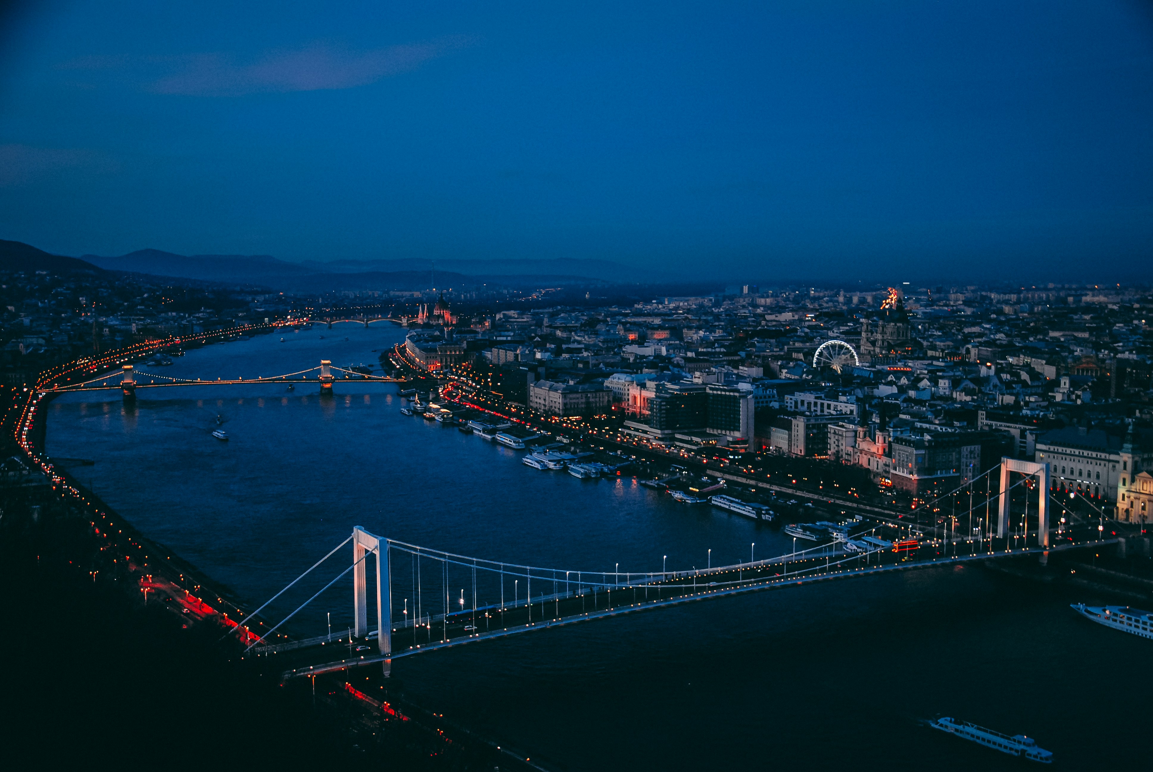 Aerial view of a cityscape with bridges and a river illuminated by city lights at dusk.