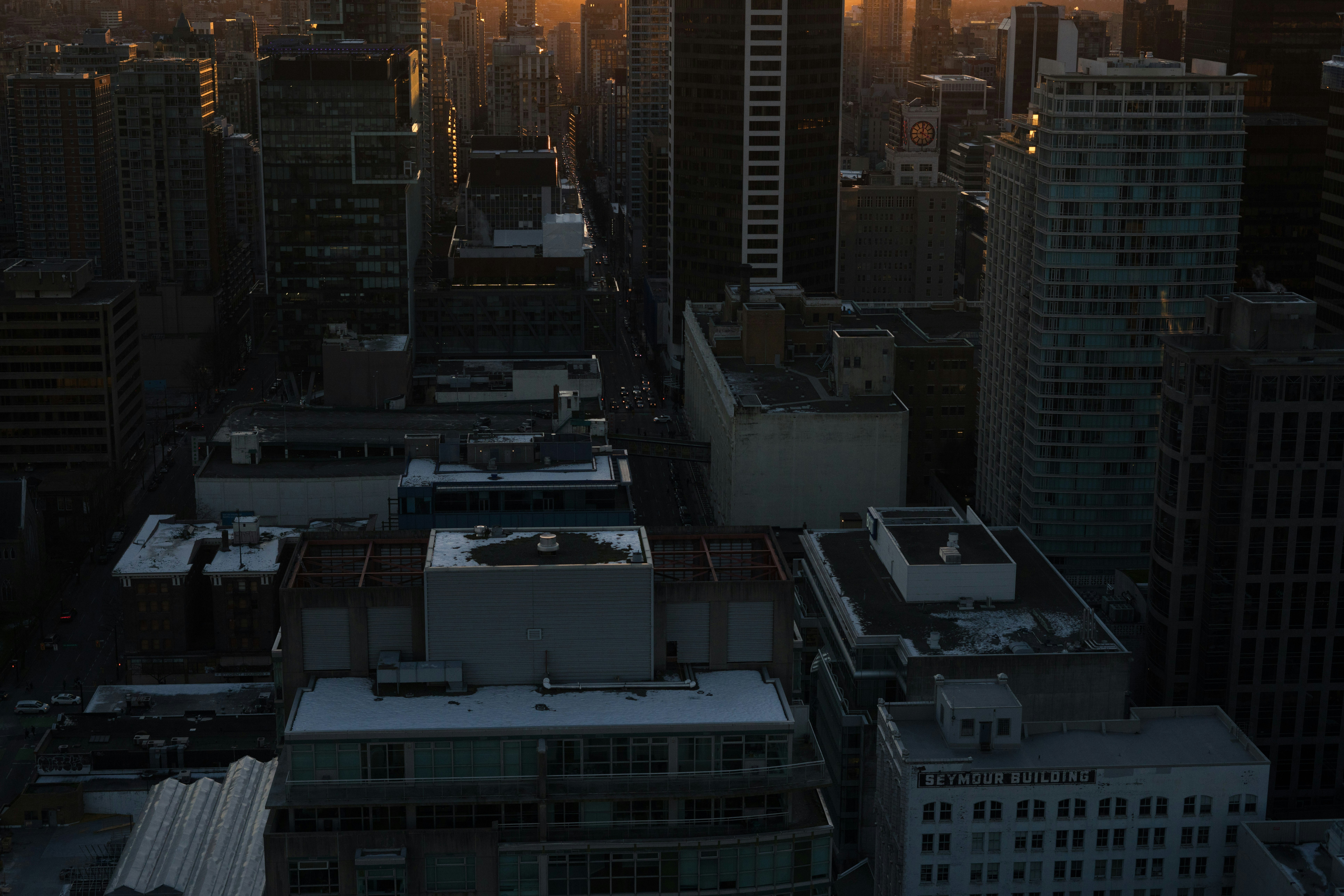 Cityscape at dusk with sunlight illuminating skyscrapers and casting long shadows over rooftops.