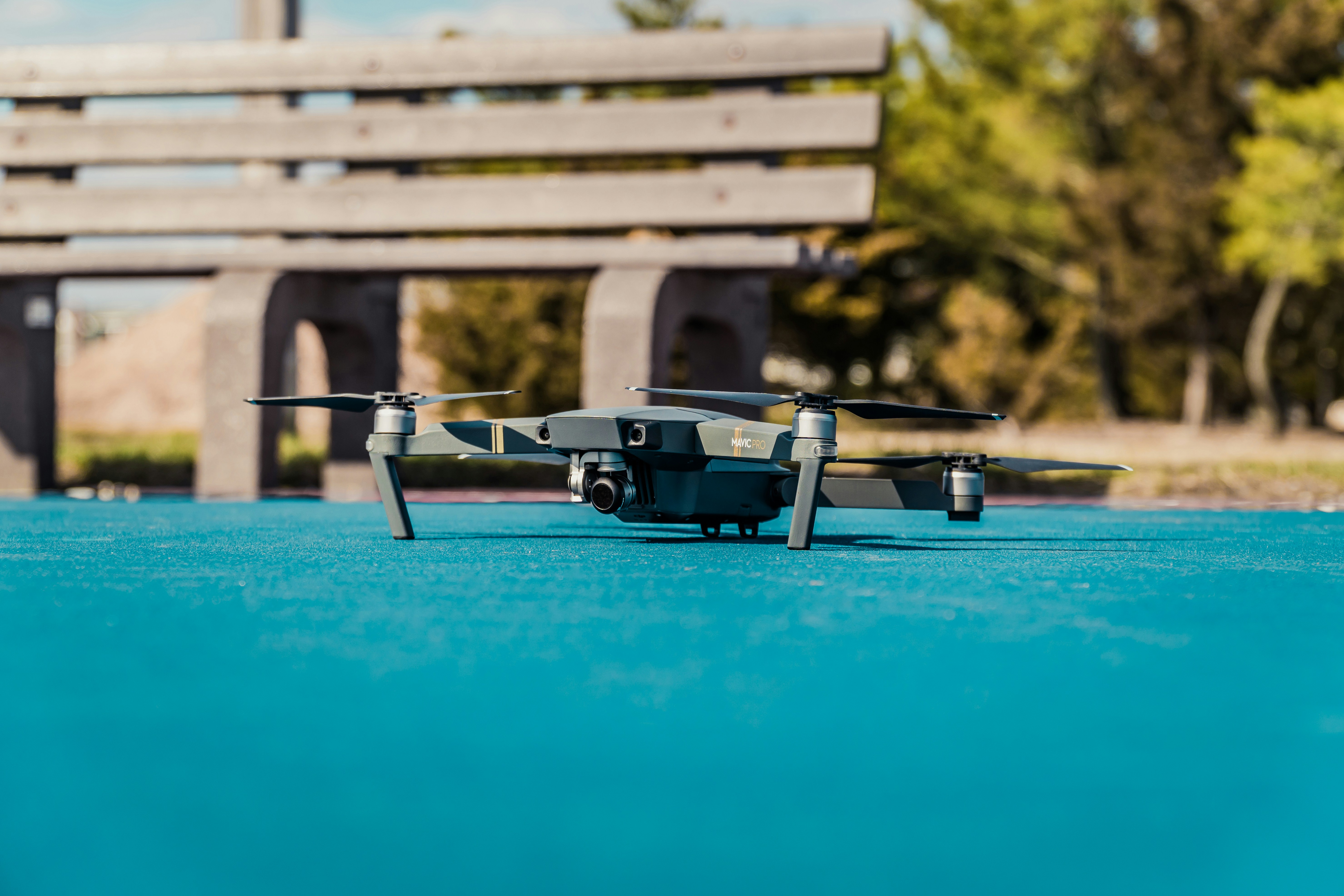 A drone positioned on a vibrant blue surface with a park bench in the background, showcasing modern technology in a natural setting.