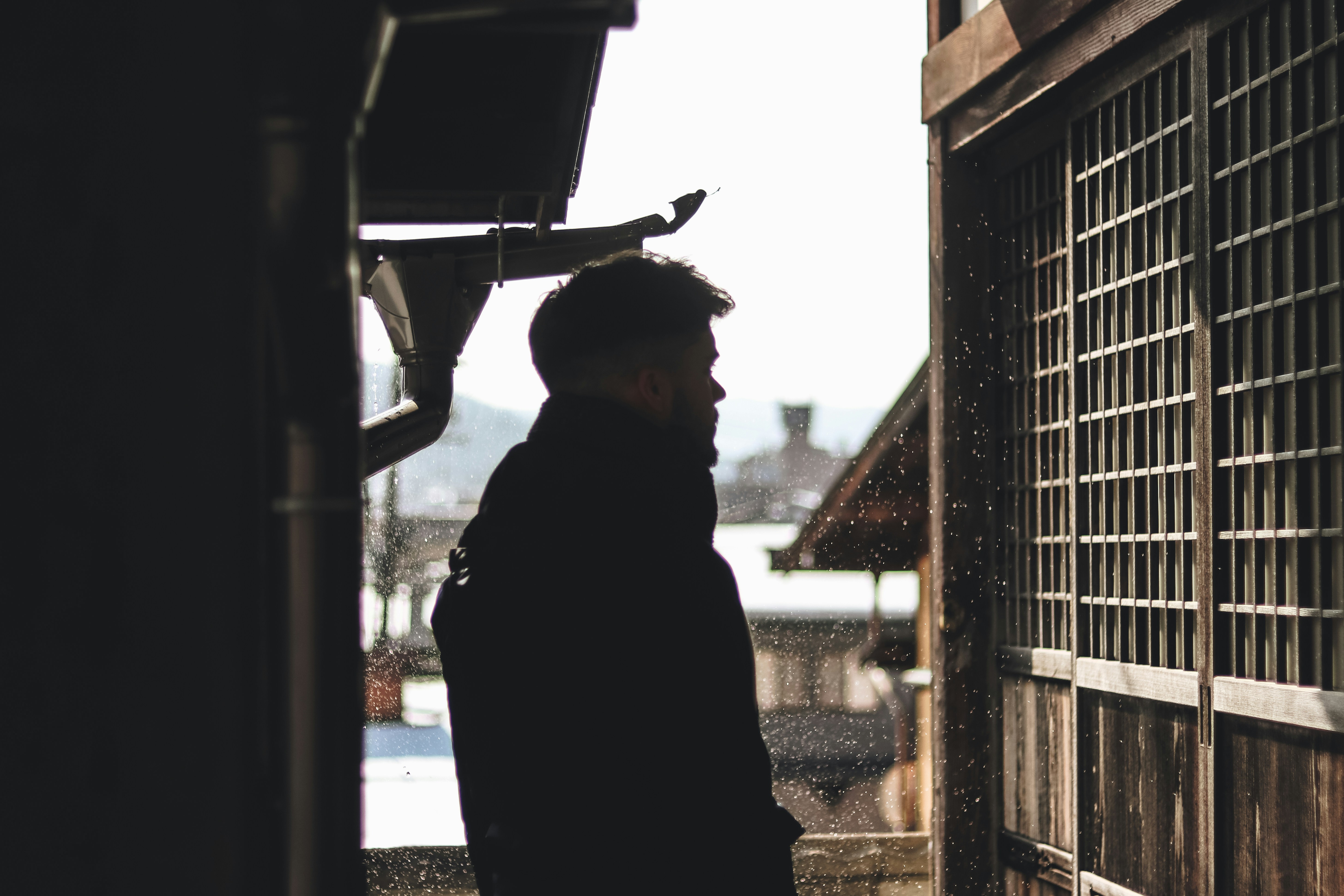 Silhouette of a man standing in a narrow alley, gazing at a window with a traditional wooden lattice.