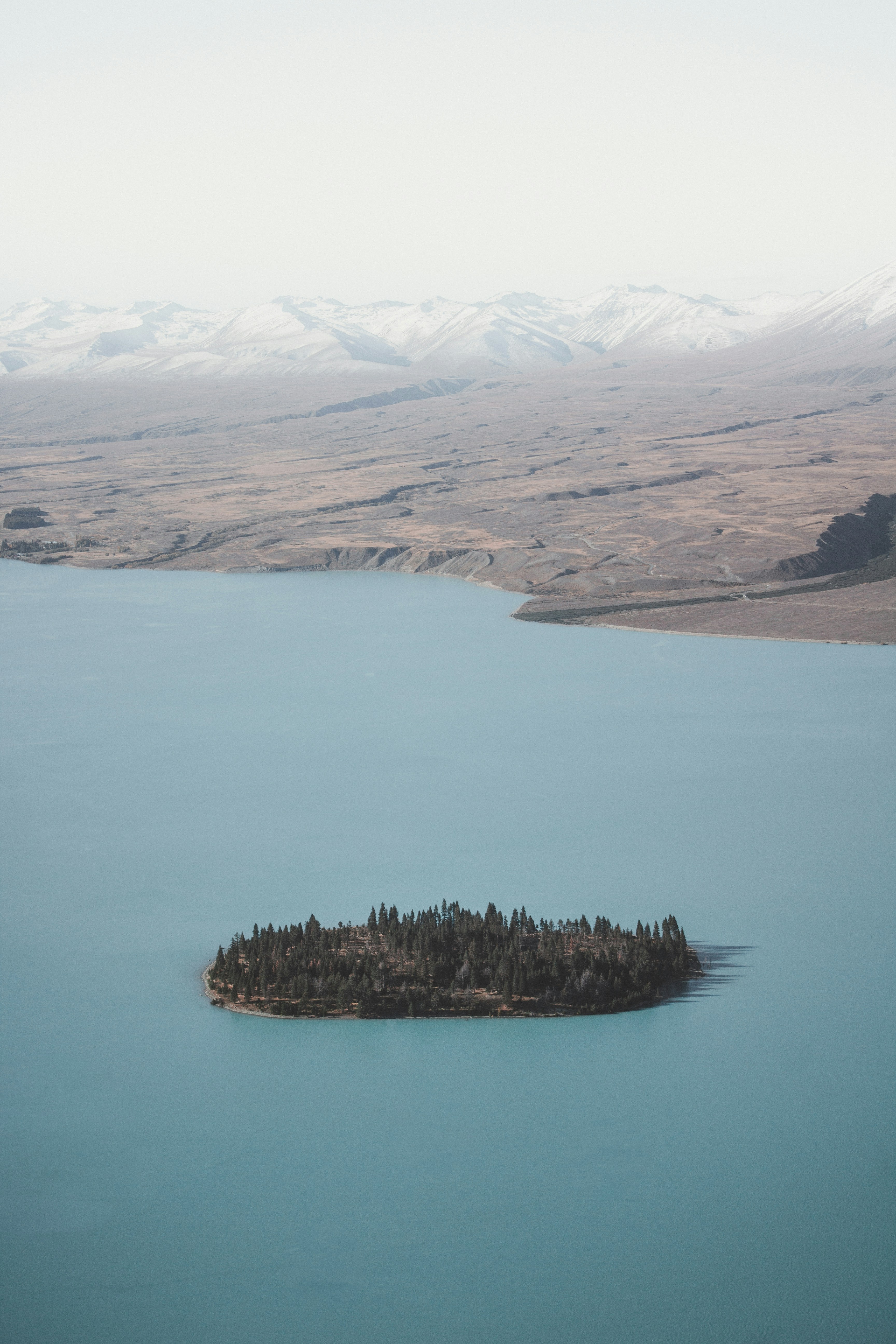 Pine Island in a Turquoise Glacier Lake Beneath Snowbound Peaks