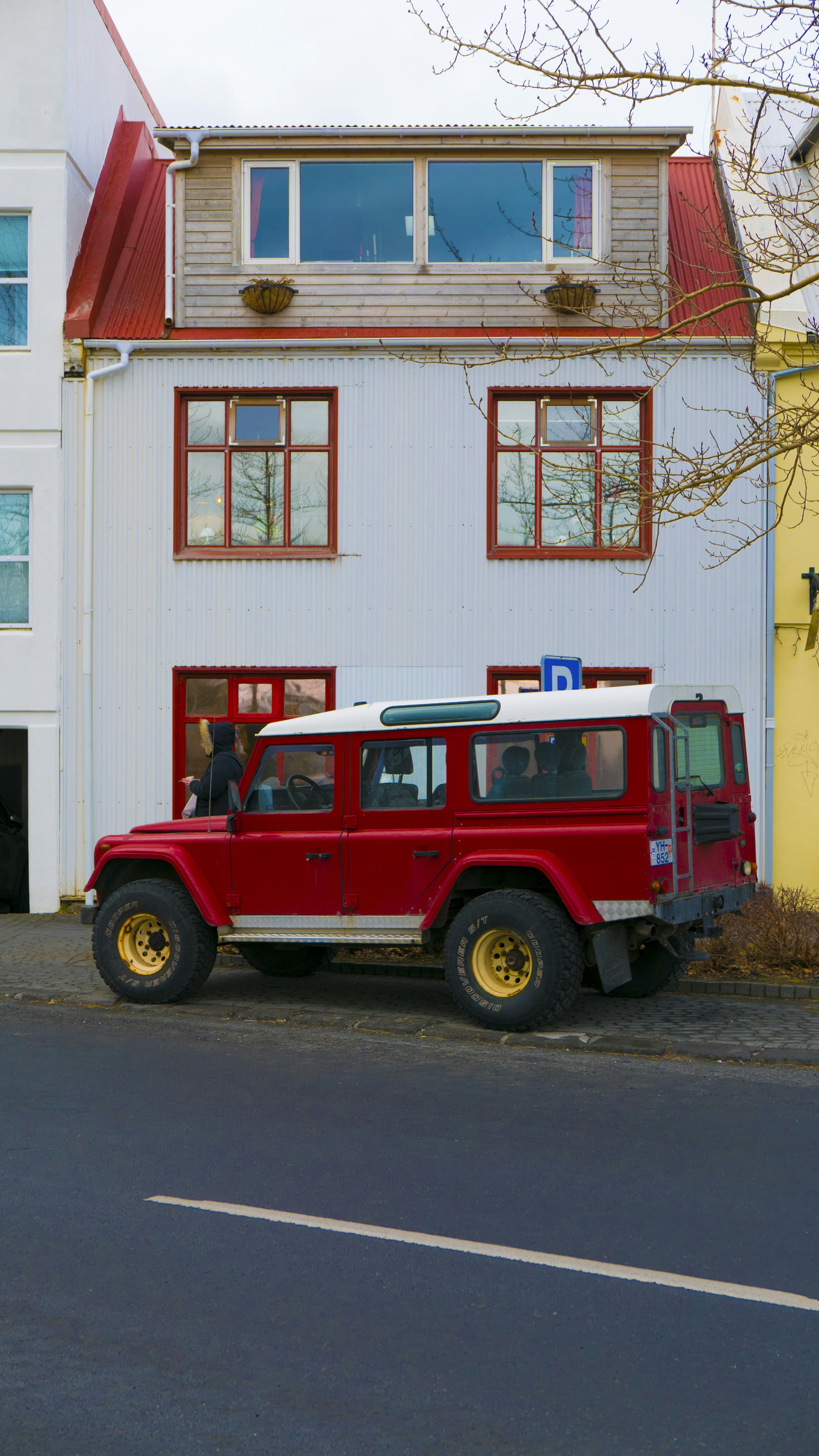 A vibrant red off-road vehicle parked beside a charming building with colorful windows in an urban setting.