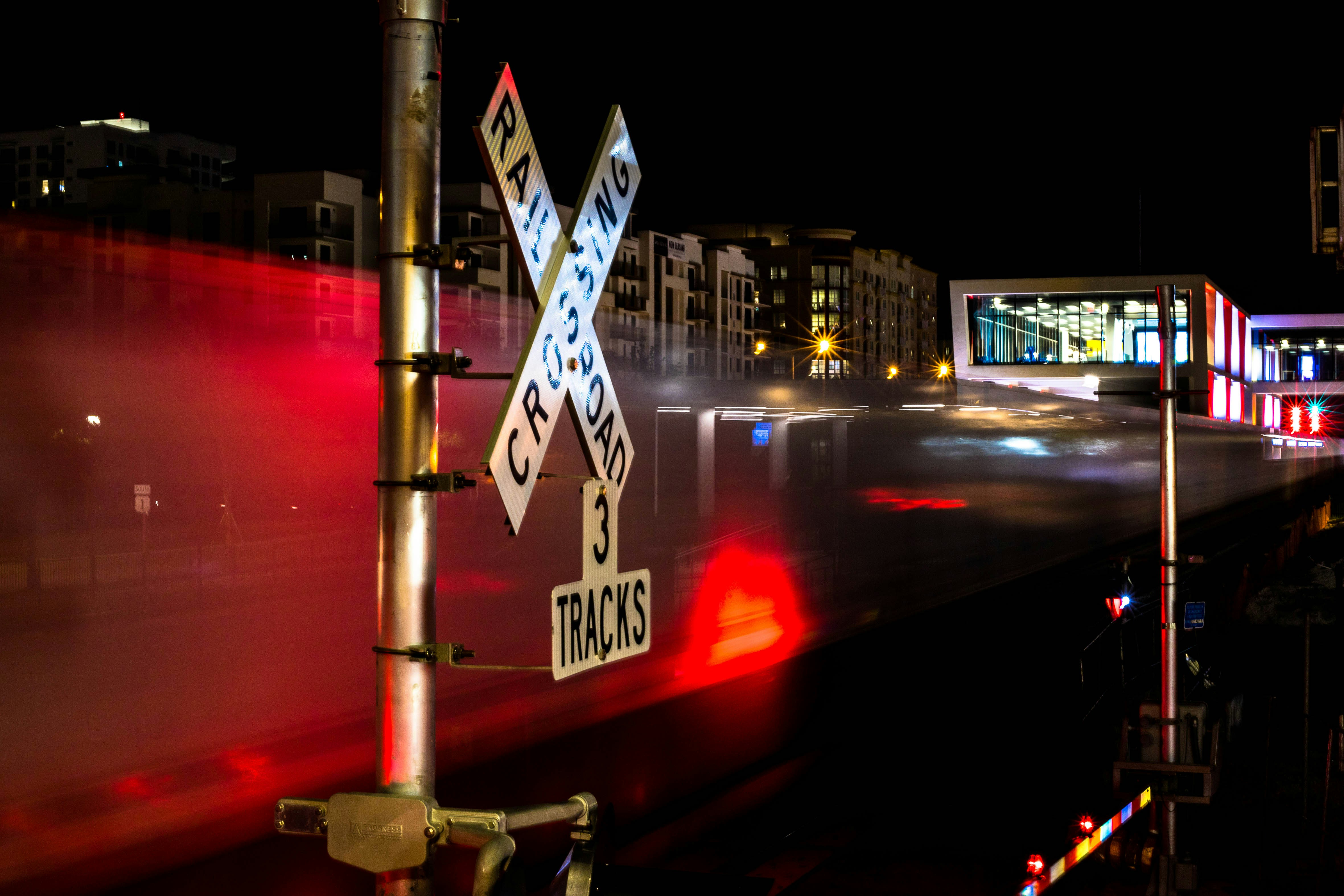 Long exposure of a train passing a railroad crossing at night with red and white light trails.