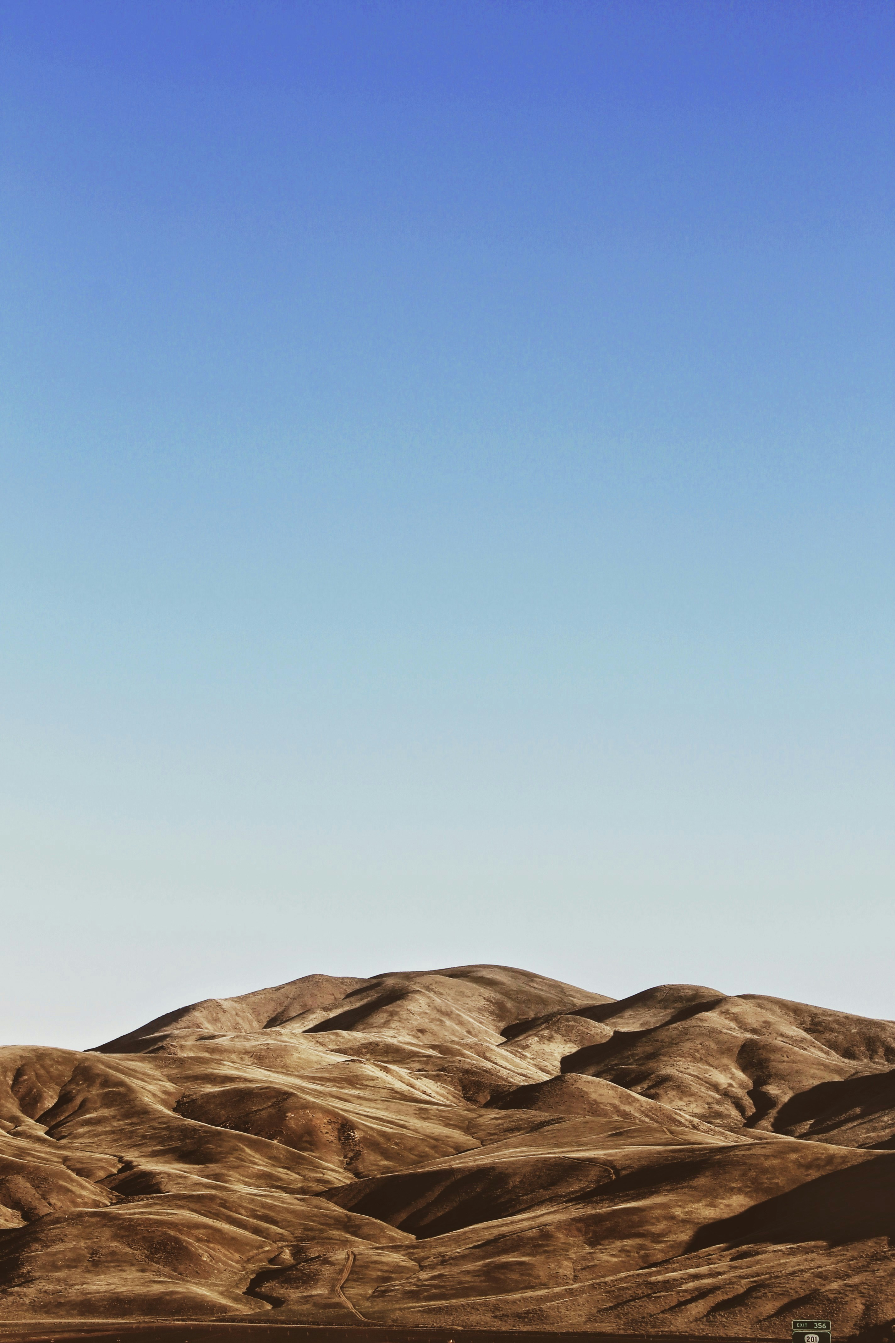 A vast expanse of rolling hills under a clear blue sky, showcasing the textured beauty of arid terrain.