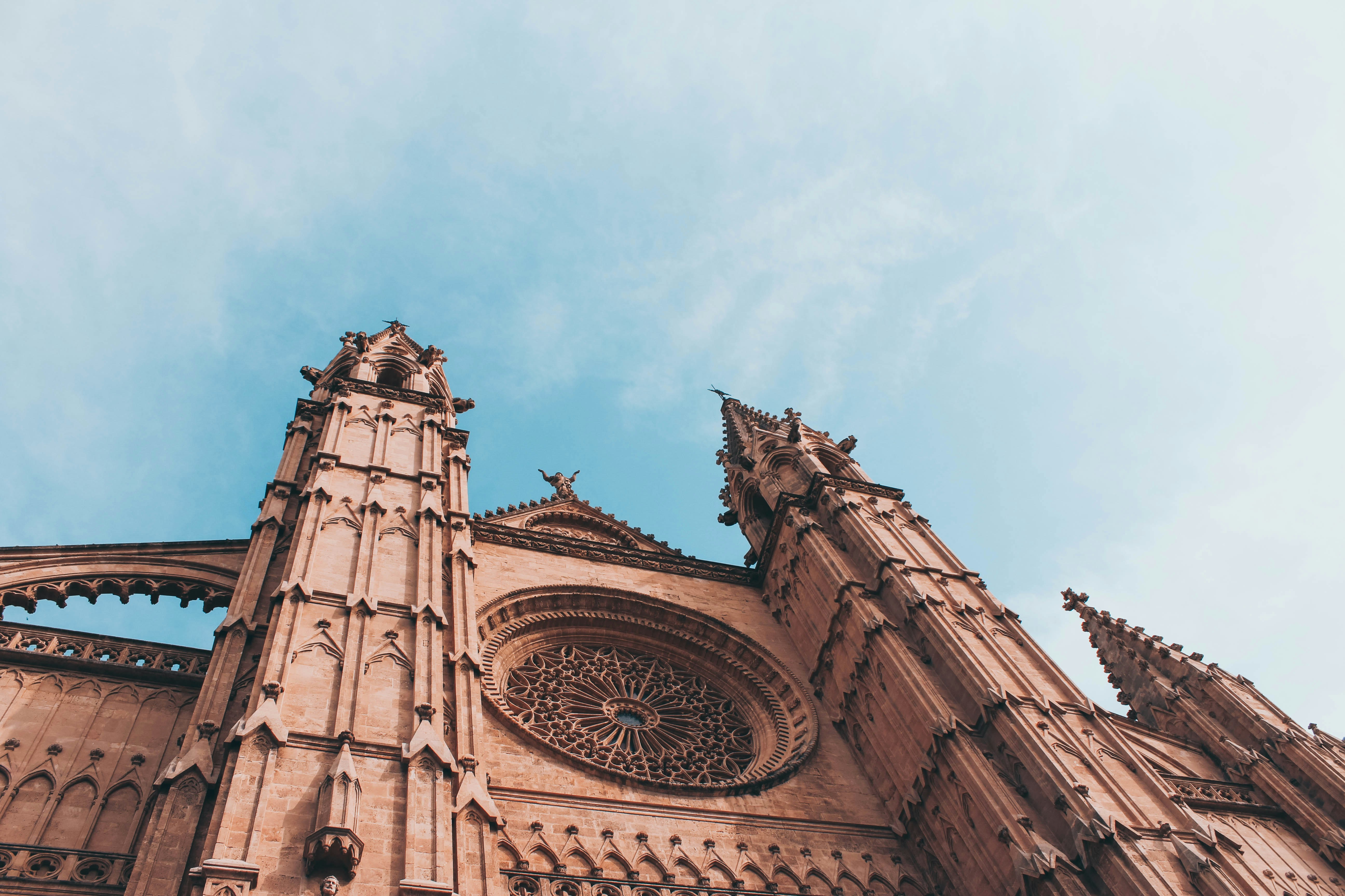 Intricate Gothic architecture of a cathedral viewed from below, highlighting its ornate spires and detailed façade against a bright sky.