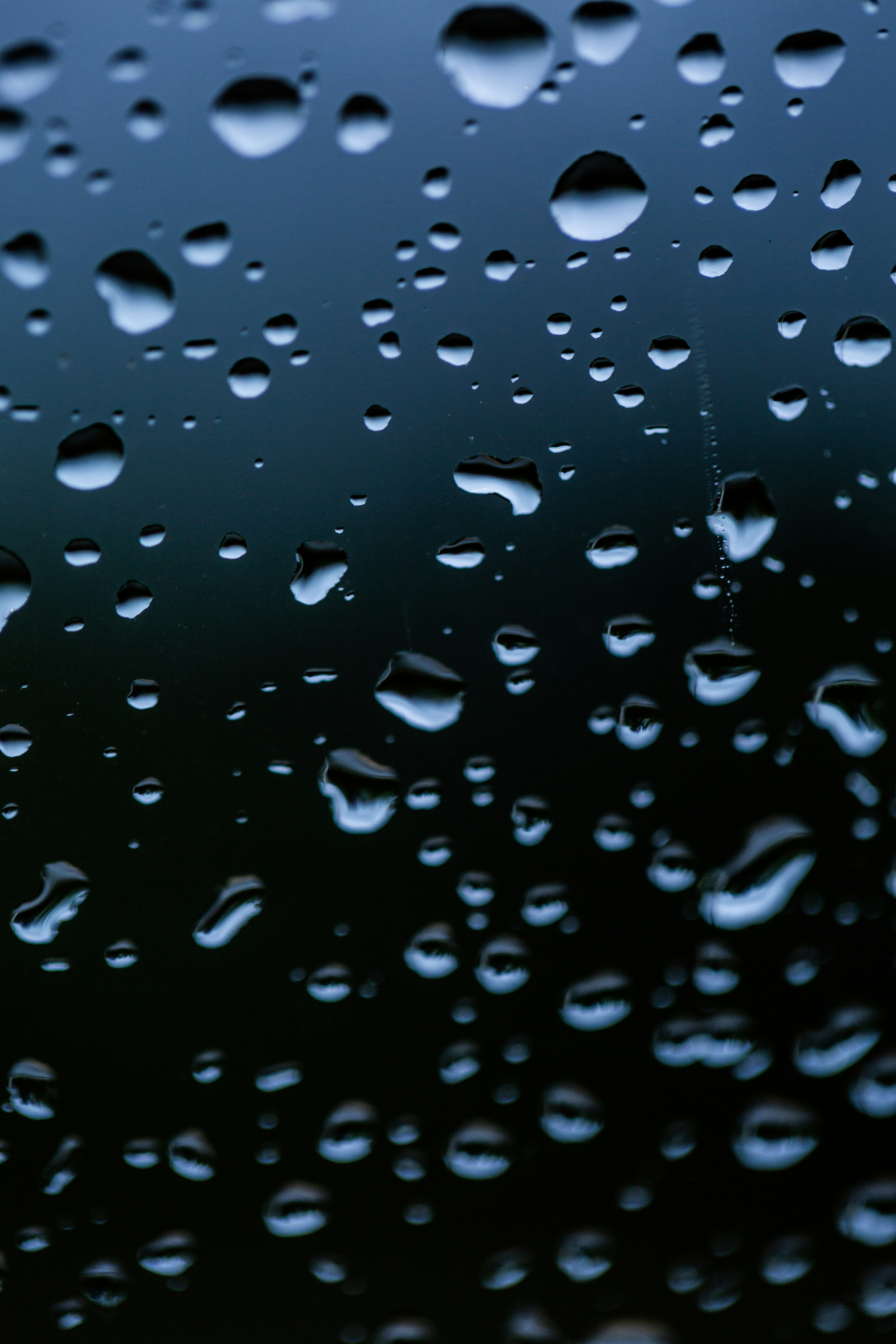 Close-up of water droplets on a glass surface, creating a textured view against a blurred dark background.