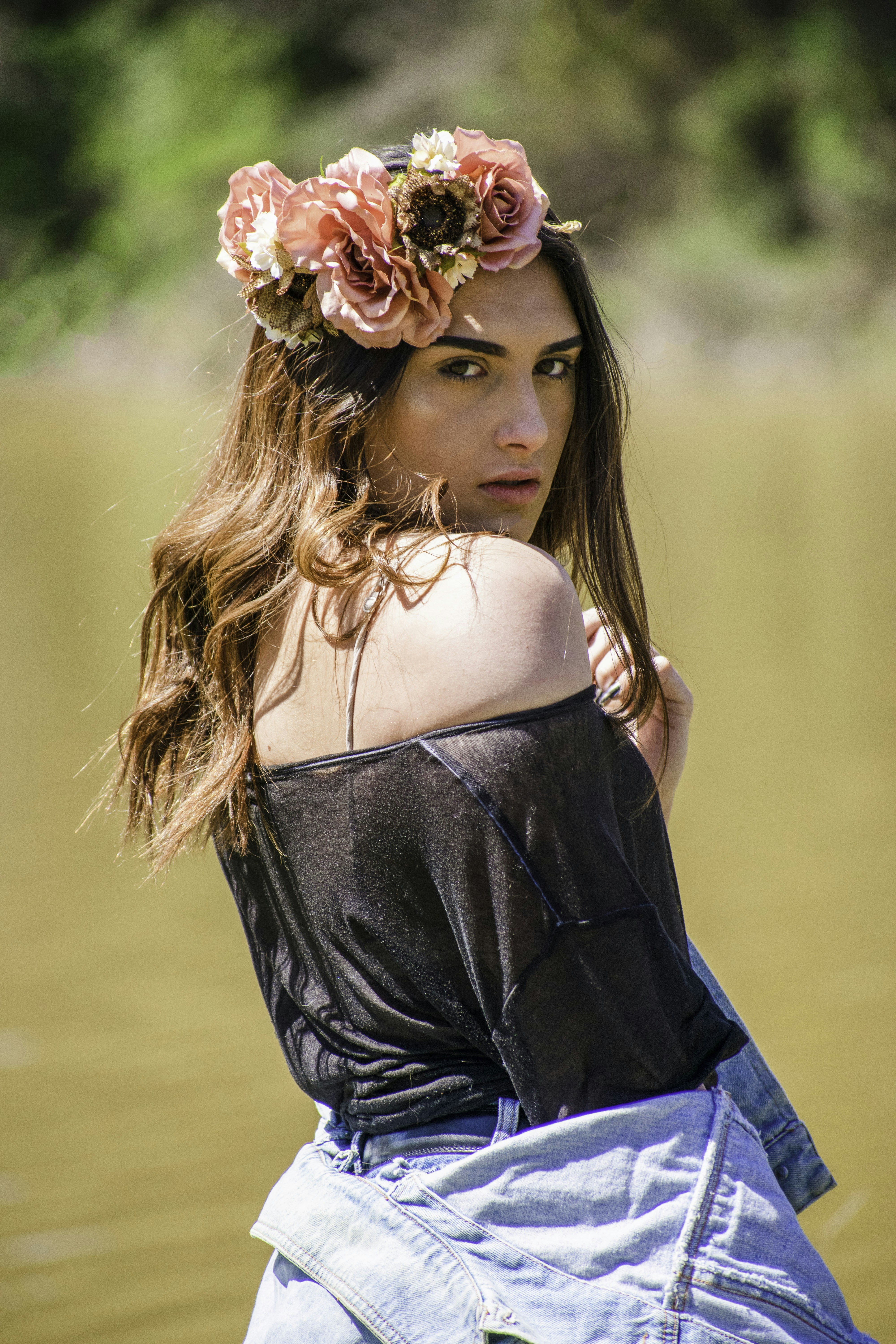 Model with a floral crown gazes over her shoulder, blending elegance with a natural backdrop. The serene water reflects the greenery around her.