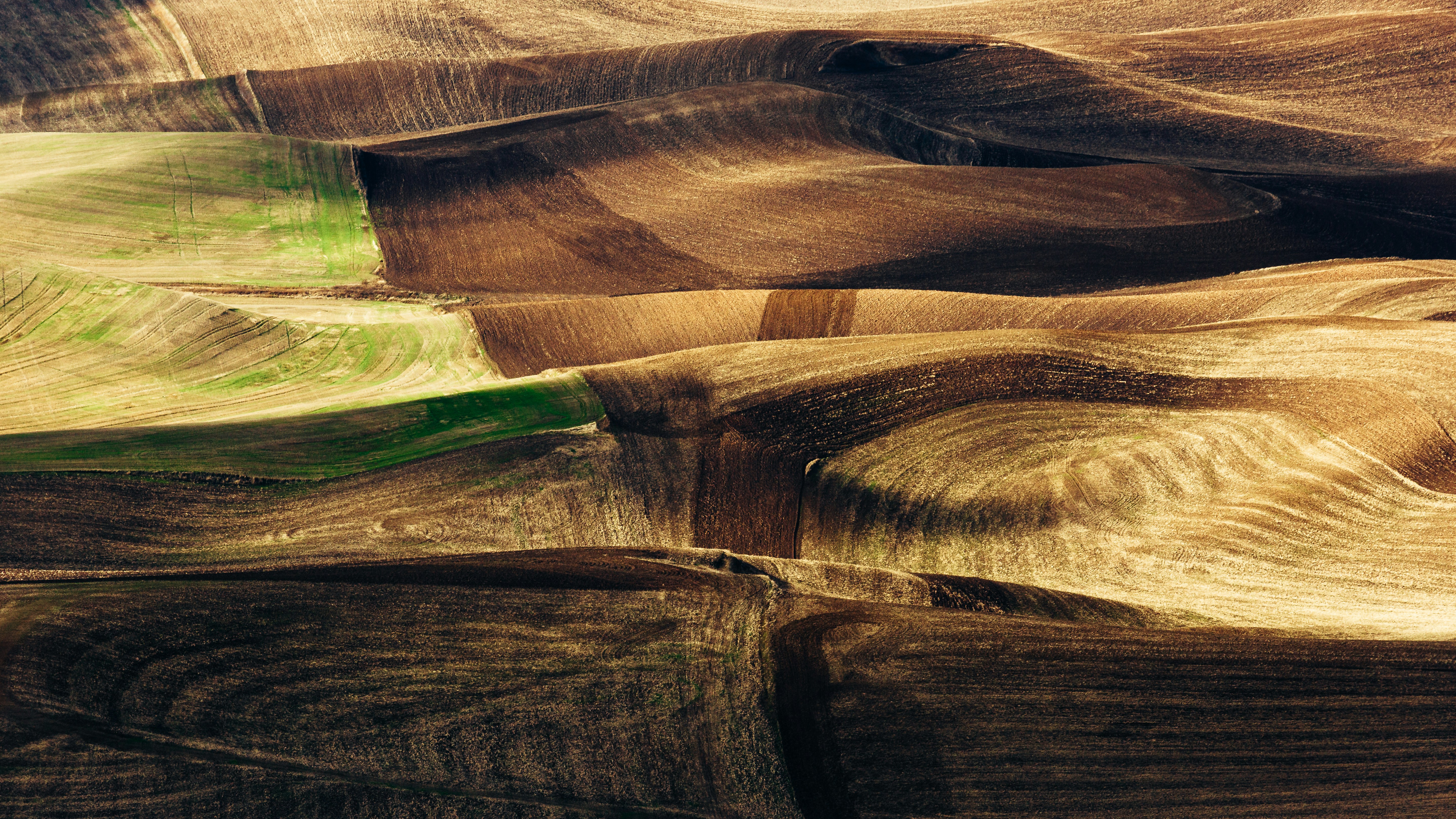 Aerial view of undulating farmland showcasing rich brown and green patterns created by crop rows and soil textures.