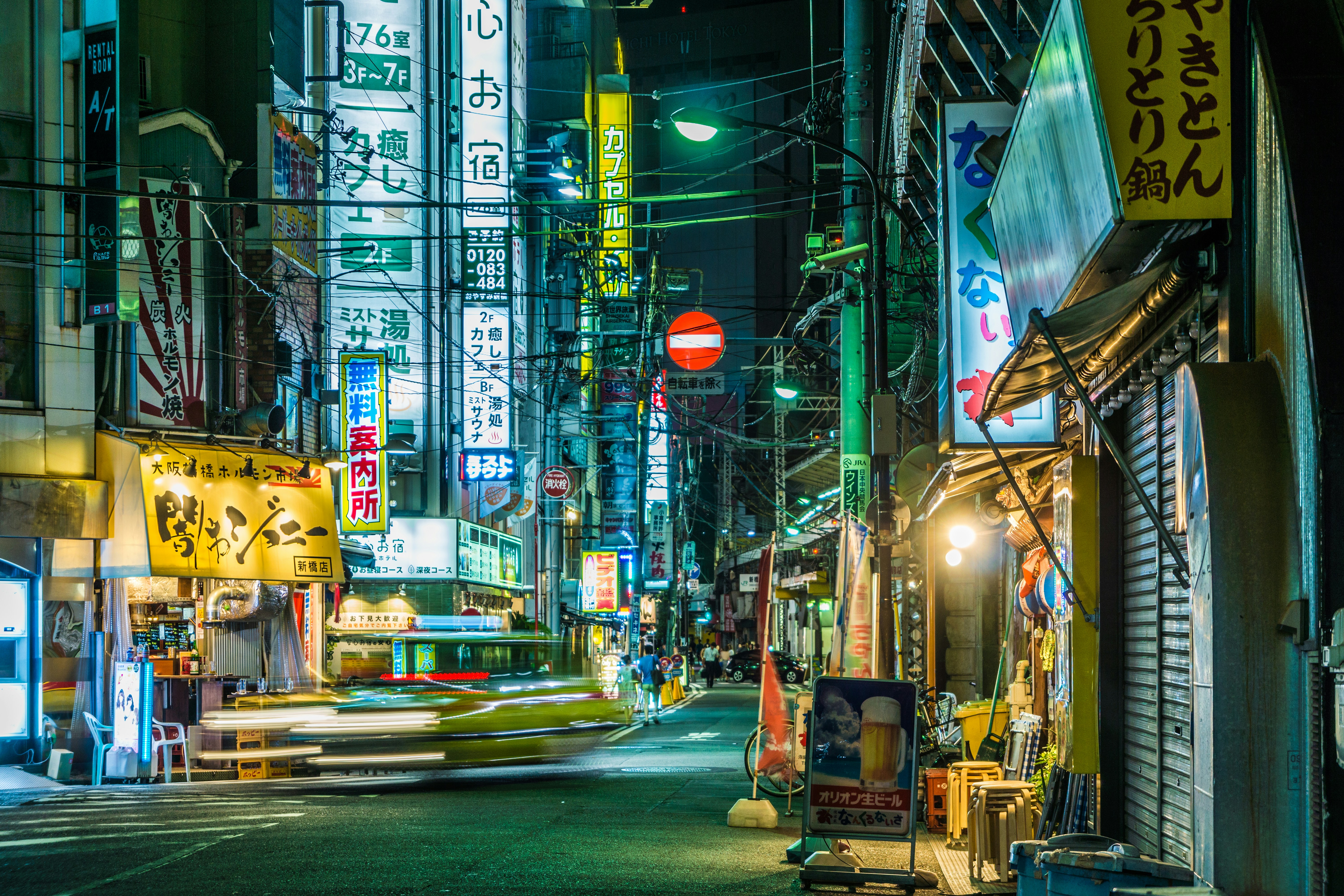 Vibrant city street illuminated by neon signs and blurred motion of a passing vehicle at night.