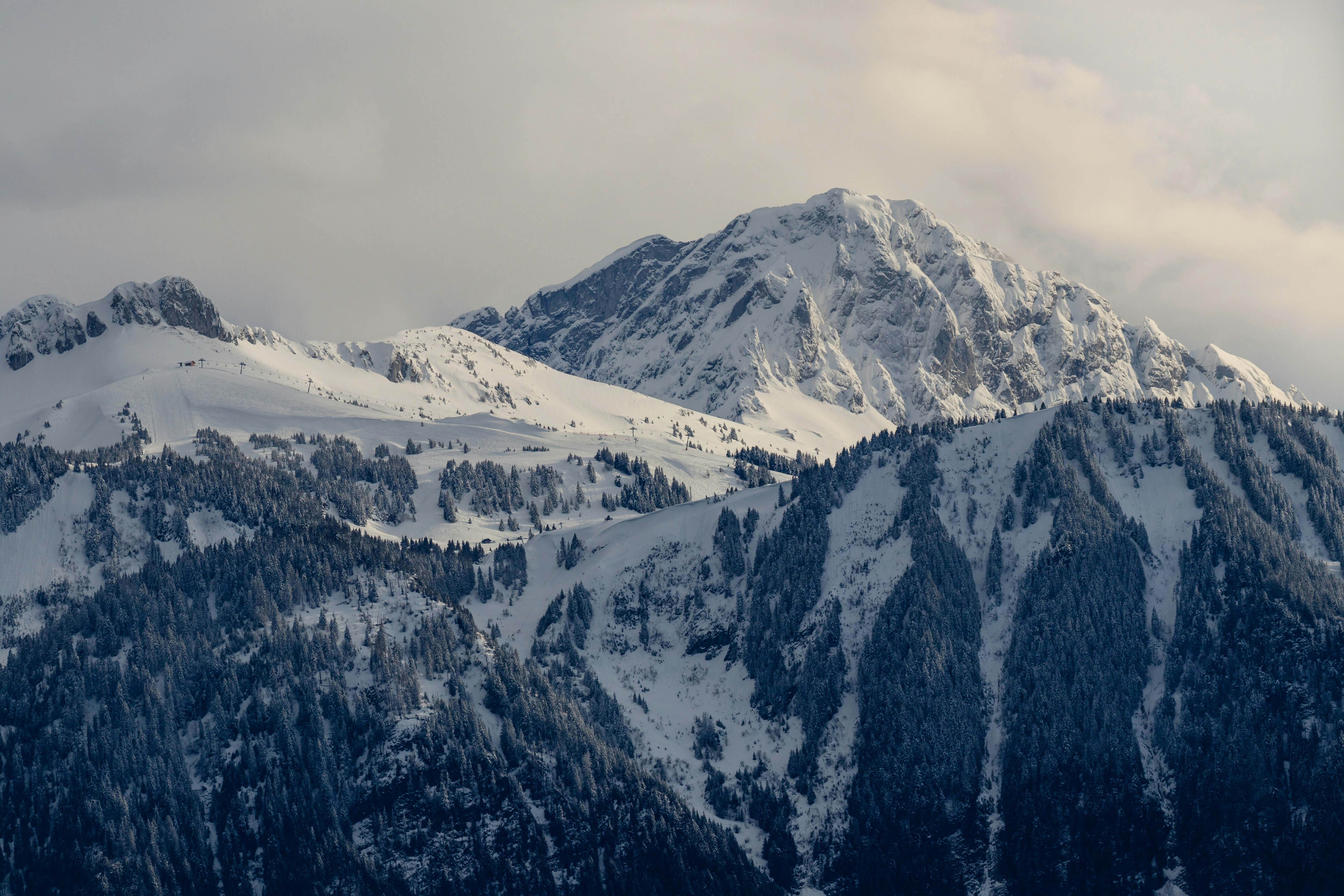 Snow-covered mountain range under a cloudy sky, highlighting the rugged terrain and serene landscape.