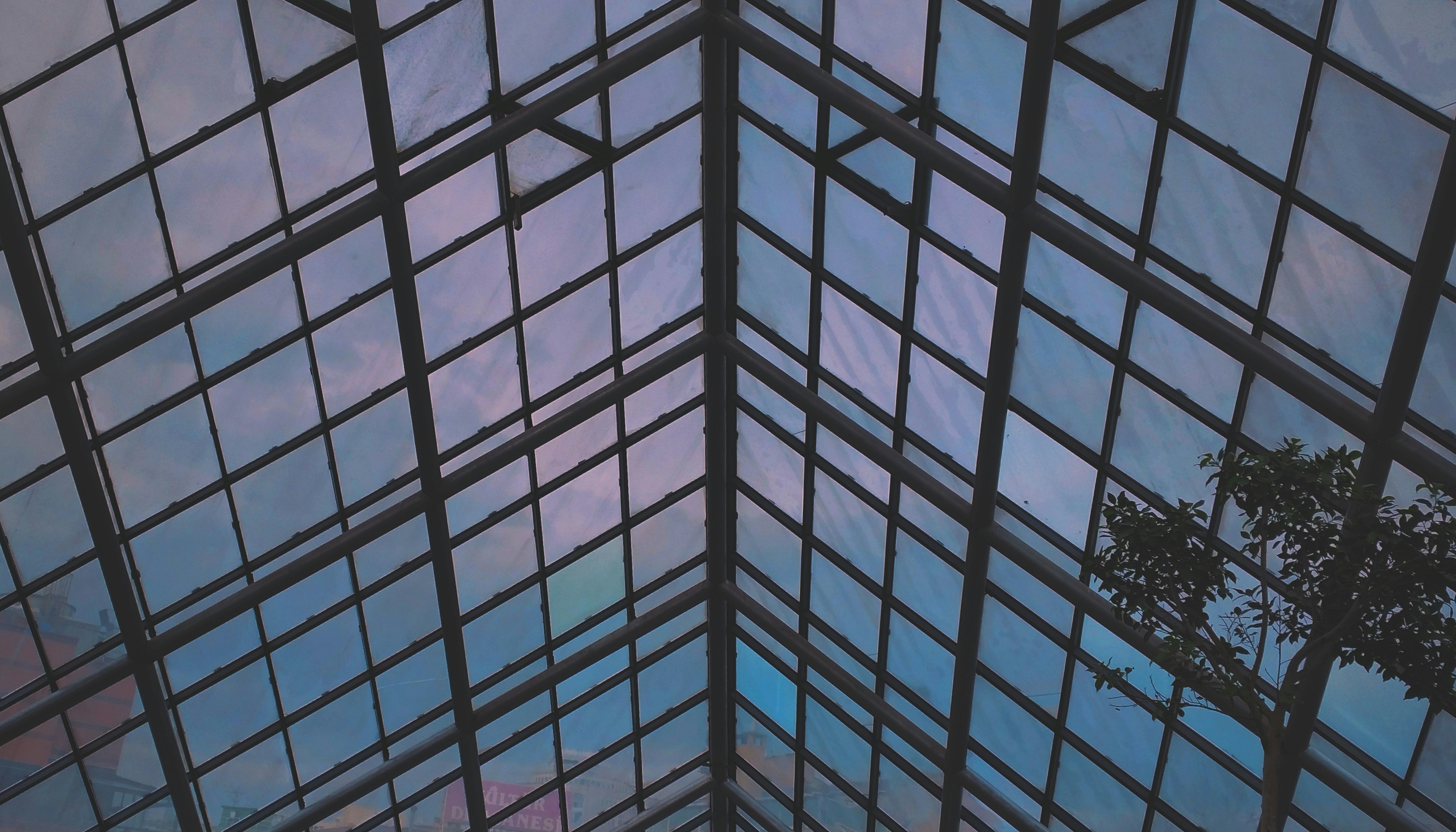 Glass ceiling with geometric patterns reflecting a blue and purple sky.