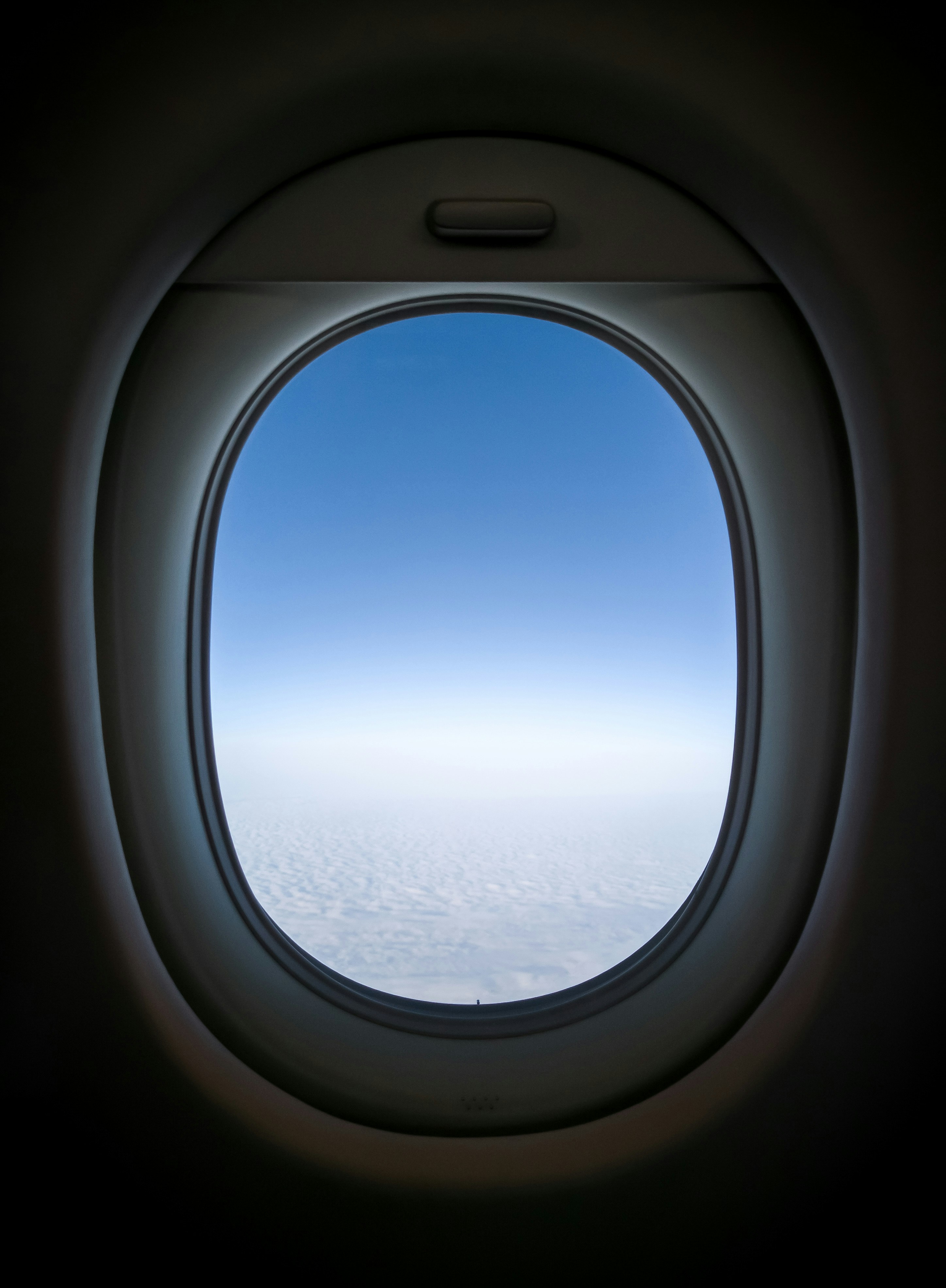 Clear view of a serene sky framed by an airplane window, showcasing a soft gradient from blue to white above a blanket of clouds.