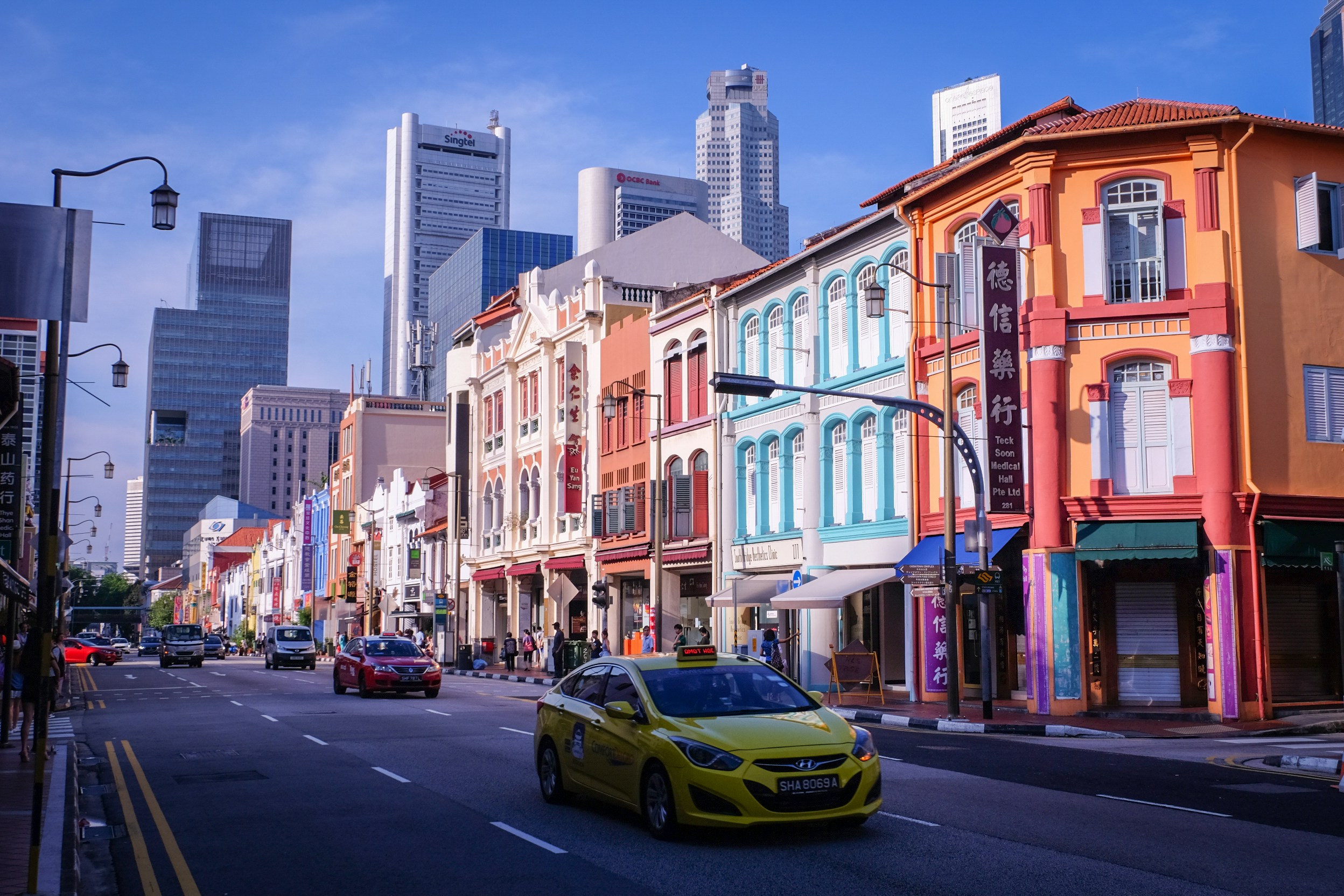 Colorful row of heritage buildings against a backdrop of modern skyscrapers under a clear blue sky.