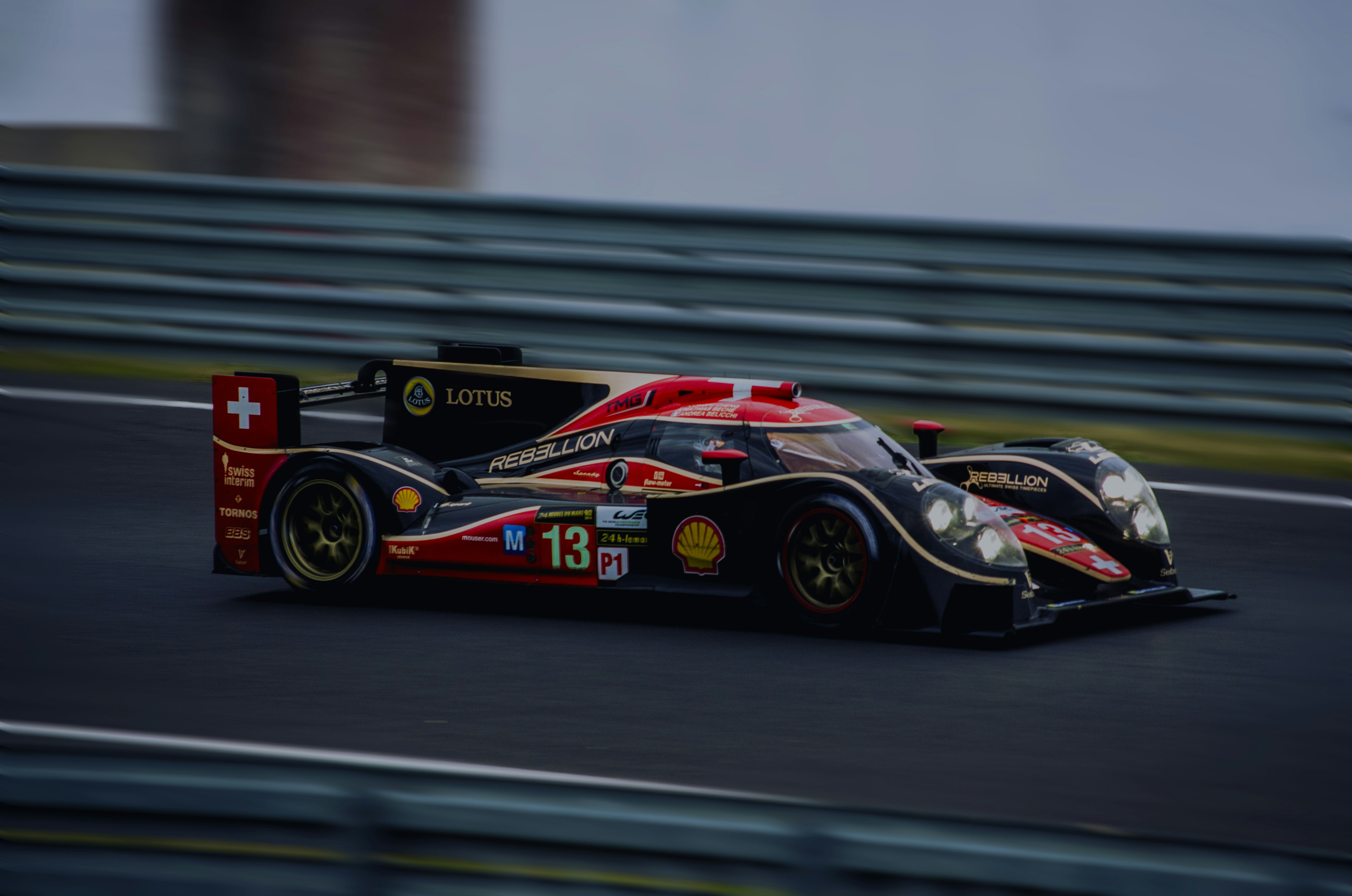 Red and black racing car speeding on a track under overcast skies.
