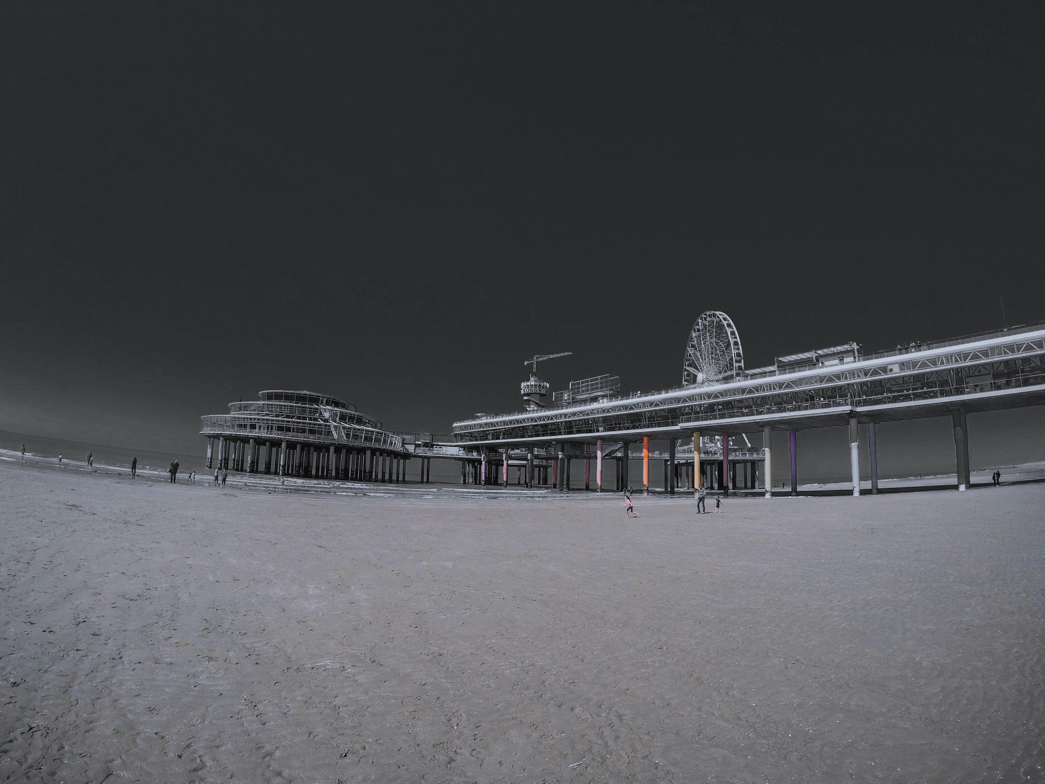 Wide-angle view of a pier with a Ferris wheel under a darkening sky.