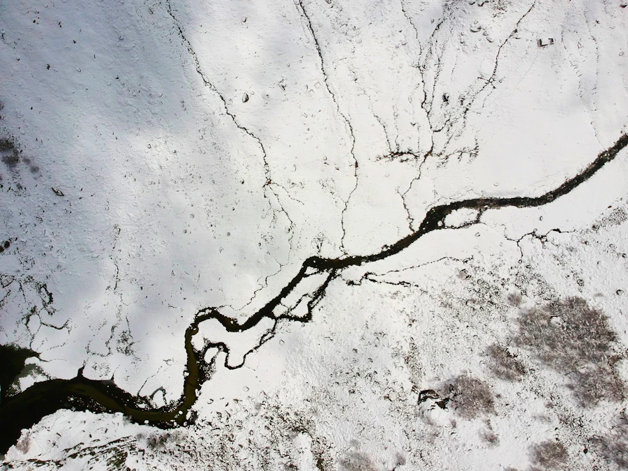 Aerial view of a dark river cutting through a snow-covered landscape.