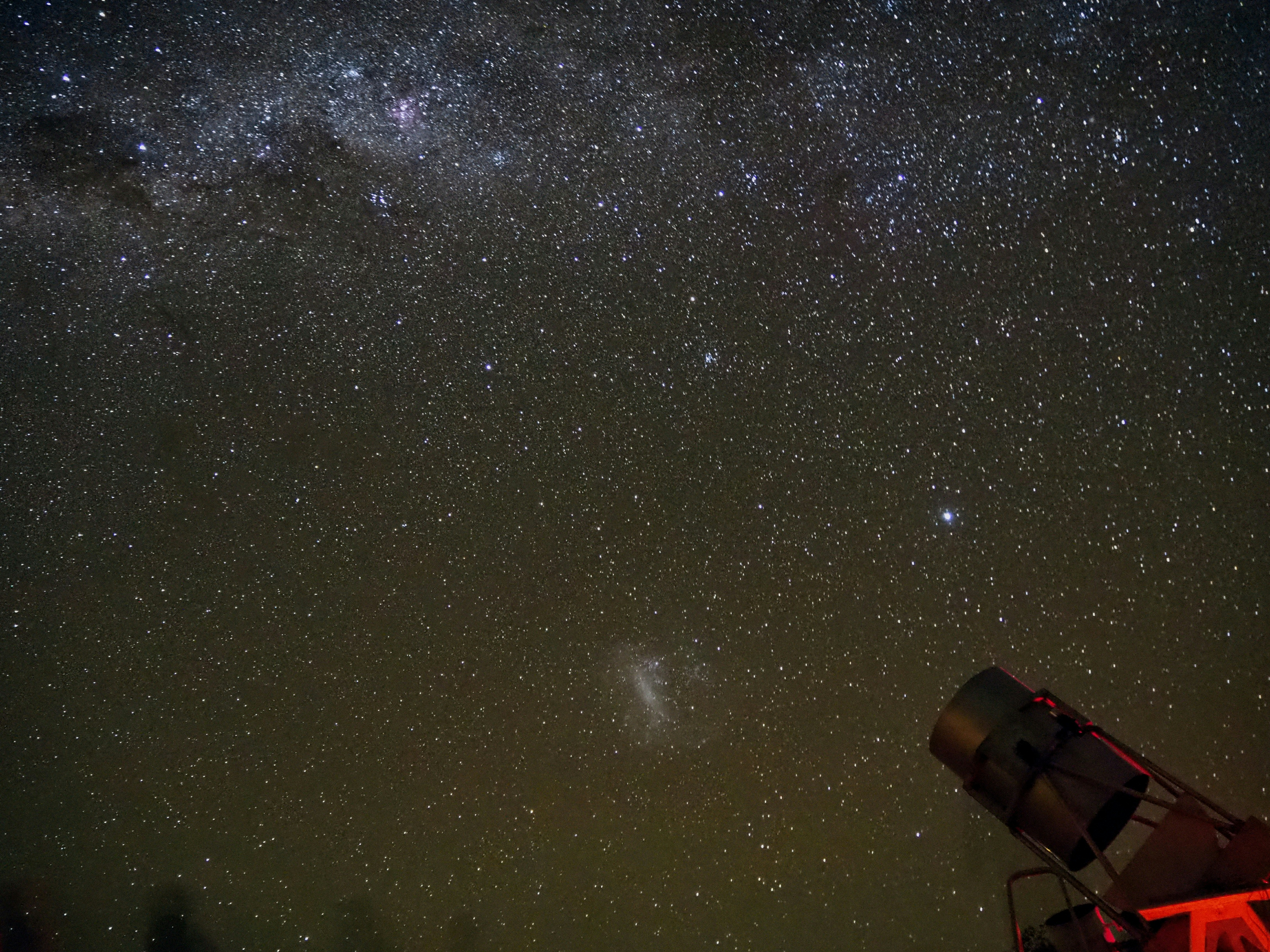 A telescope aimed at a star-filled sky, showcasing the Milky Way and distant galaxies. The scene captures the vastness of the universe.