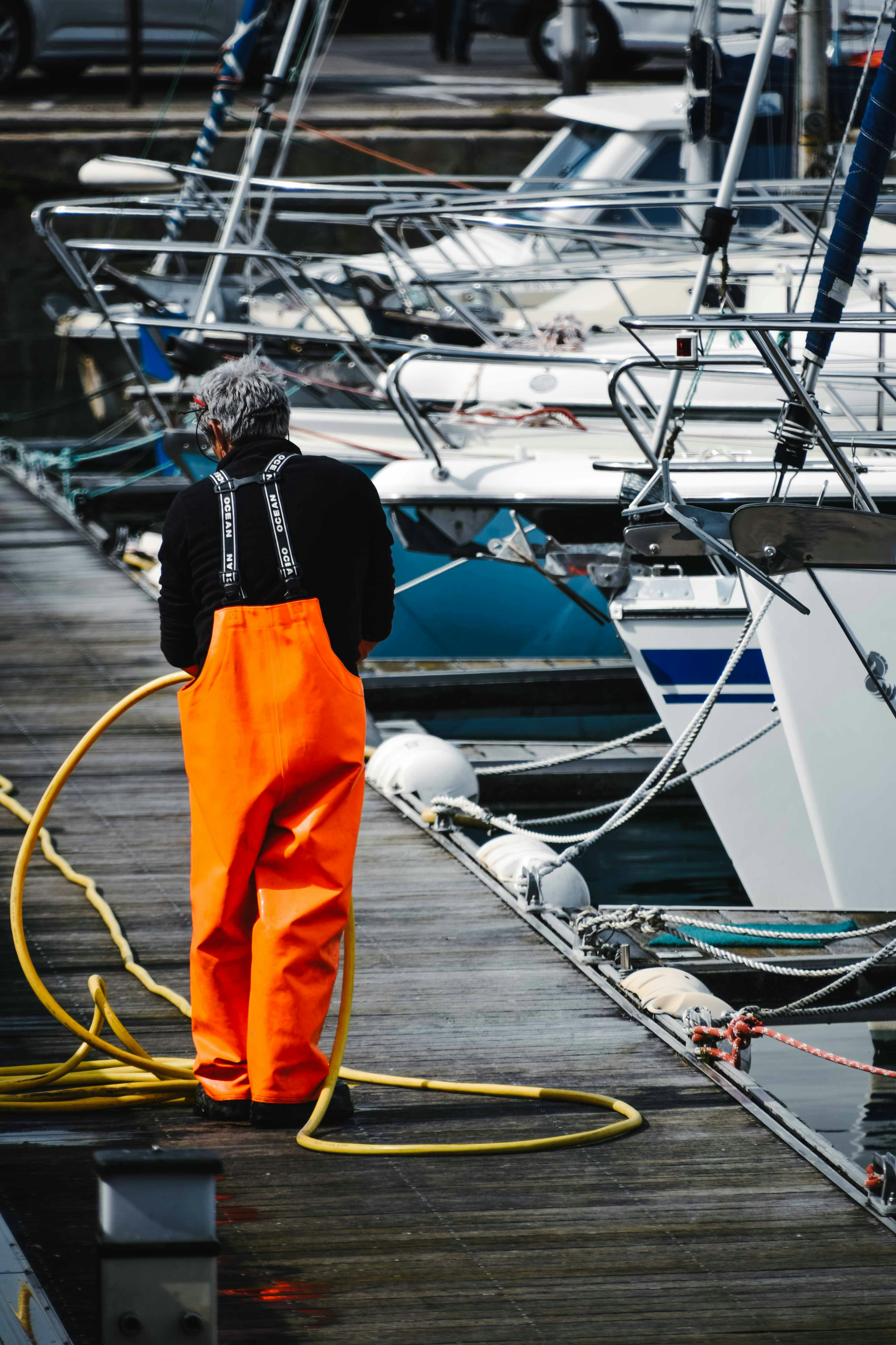 Neon Orange Overalls on a Marina Dock, Standing Amid Idle Sailboats