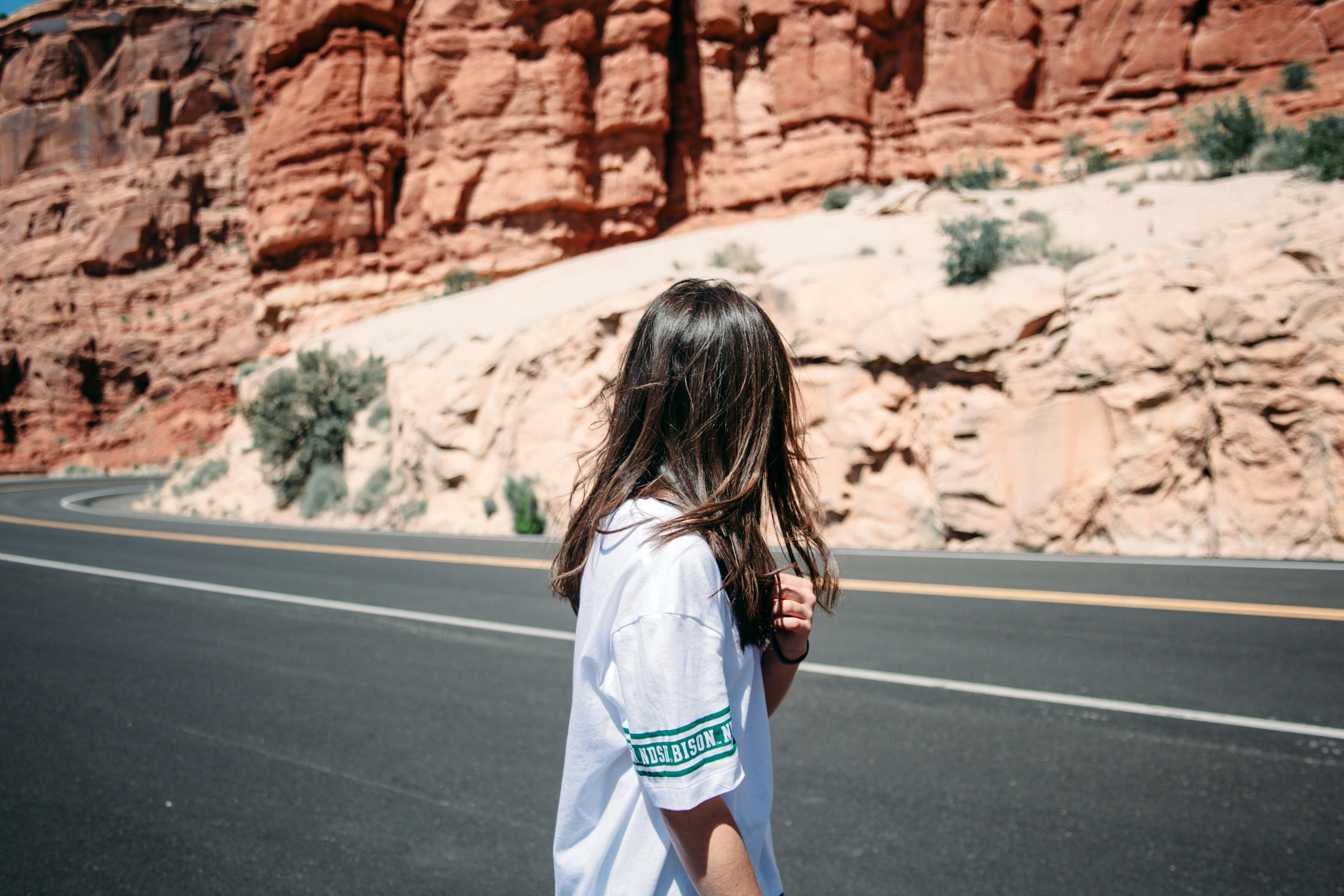 A person stands on the roadside, gazing at the towering red rock formations. The winding road invites exploration.