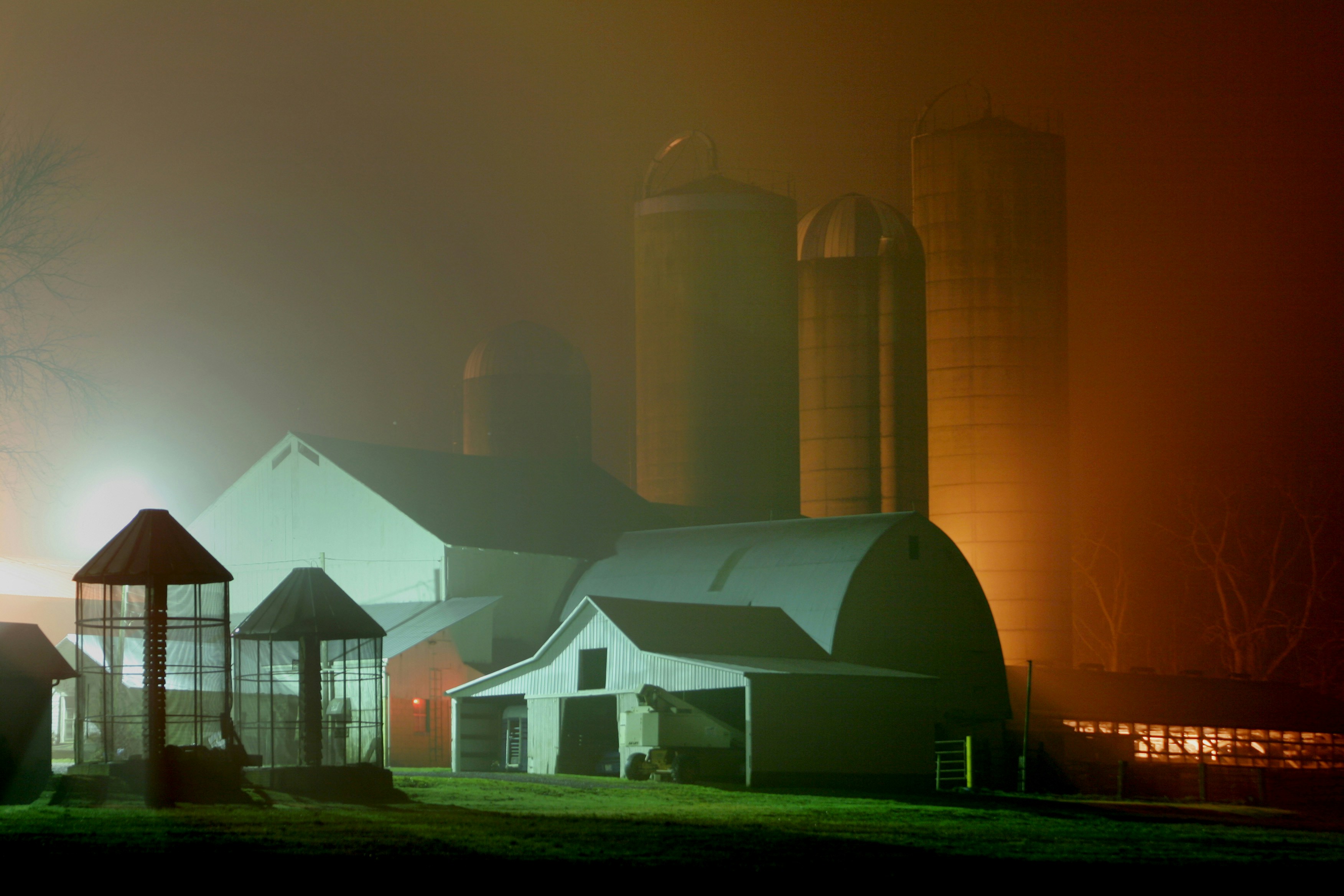 Farm buildings and silos shrouded in mist under a soft, ambient light.