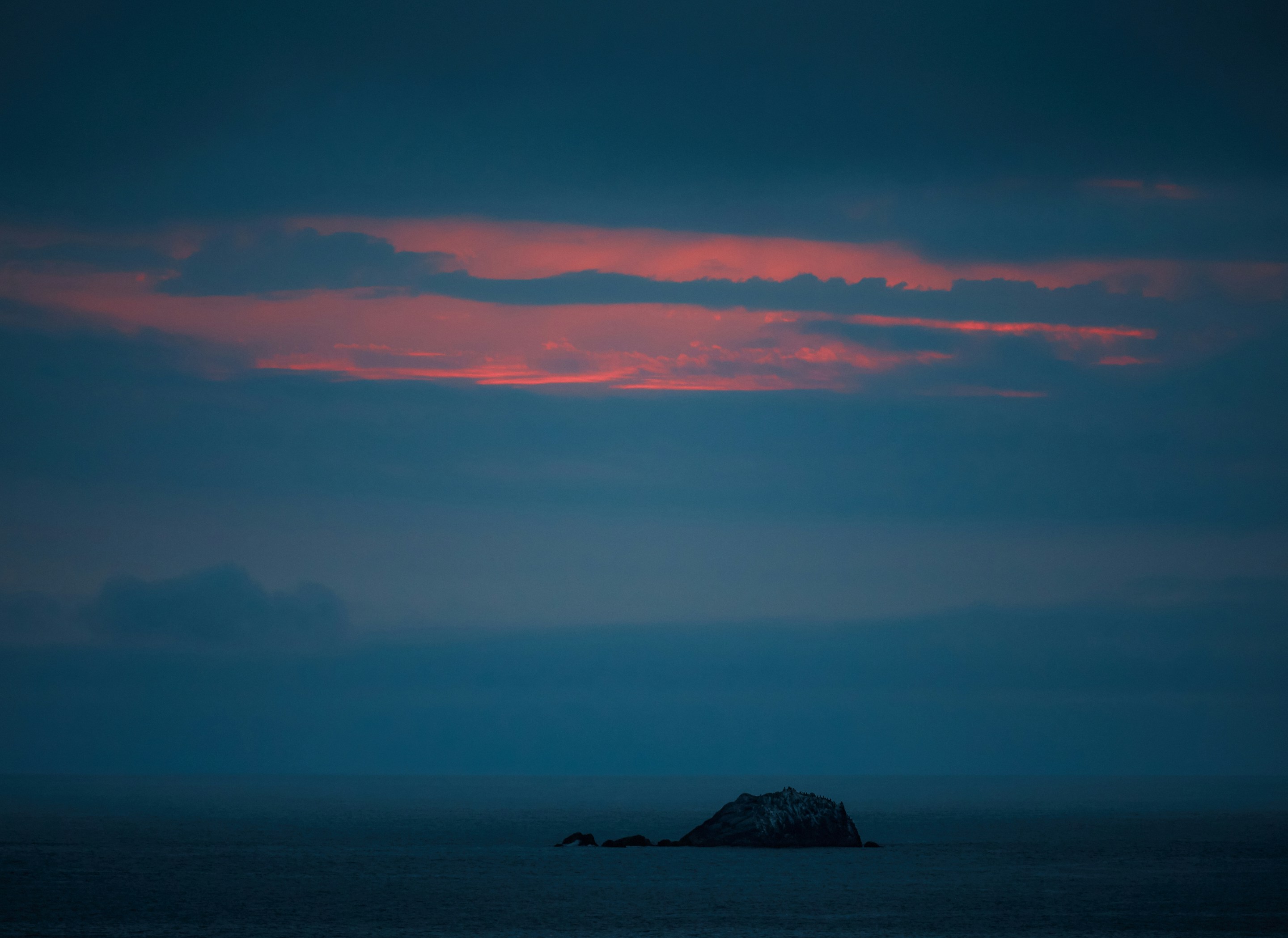 Solitary island beneath vibrant pink and blue twilight sky.