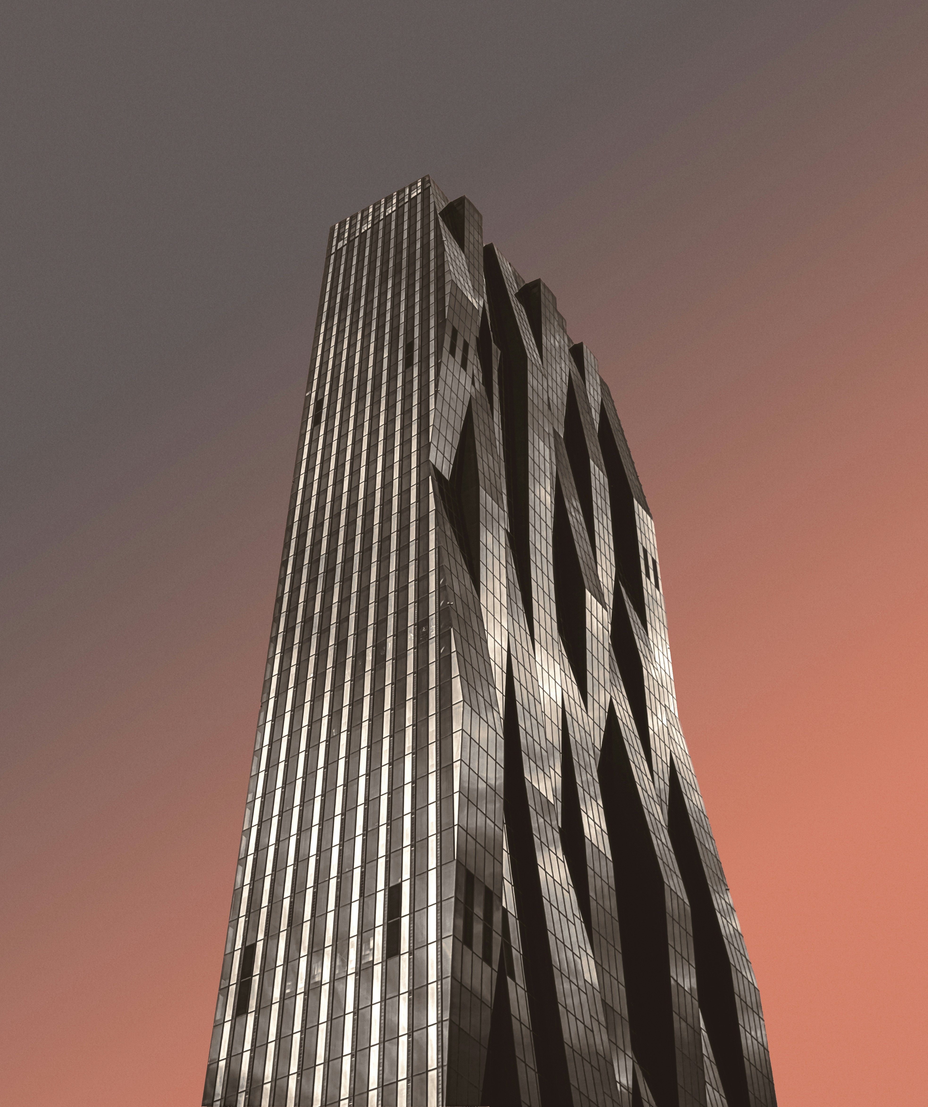 A sleek, angular skyscraper rising against a gradient sky, showcasing contemporary design elements and reflective surfaces.