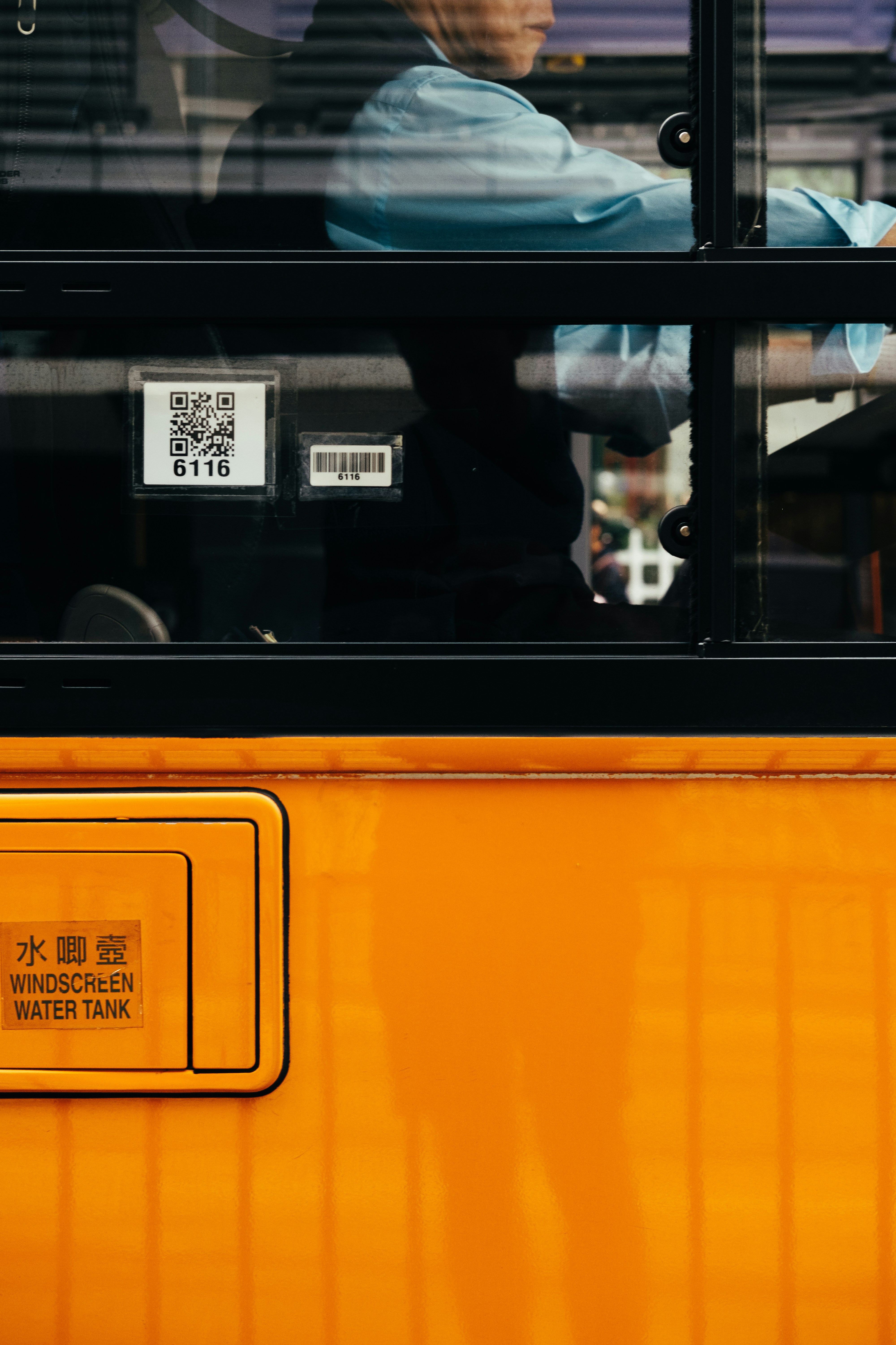Bus driver focused on the road, framed by the vibrant yellow exterior and intricate details of the vehicle's features.