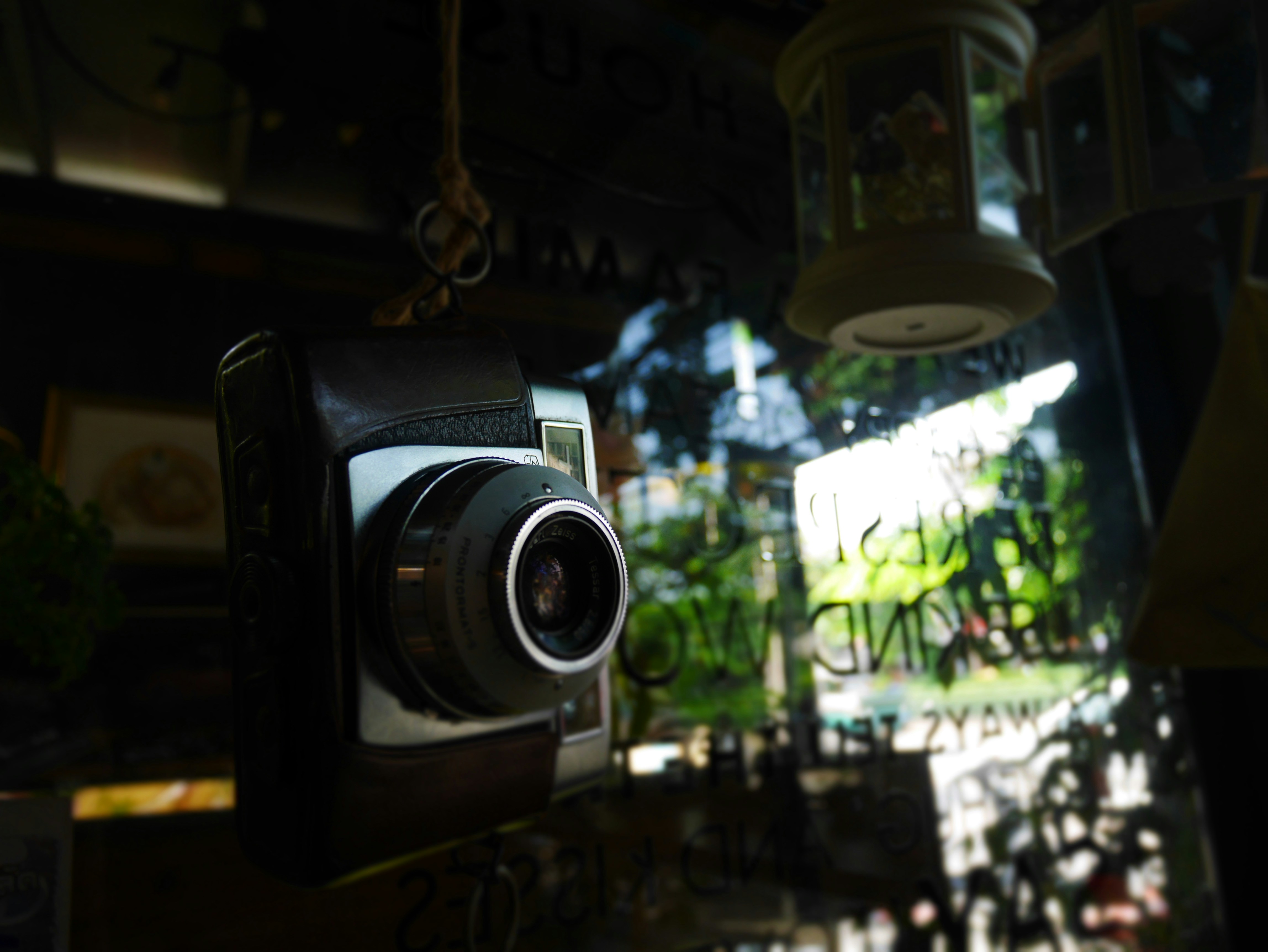A vintage camera hangs against a backdrop of greenery and reflections, showcasing the charm of classic photography equipment.