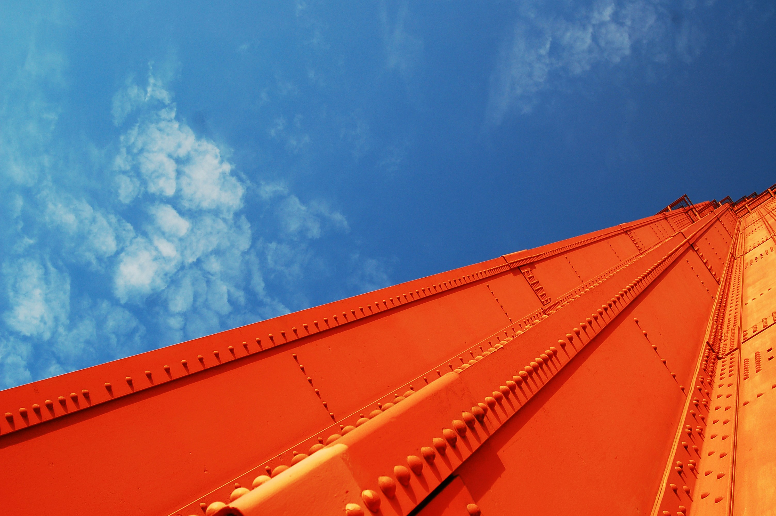 Upward view of the Golden Gate Bridge's vibrant orange tower against a bright blue sky.