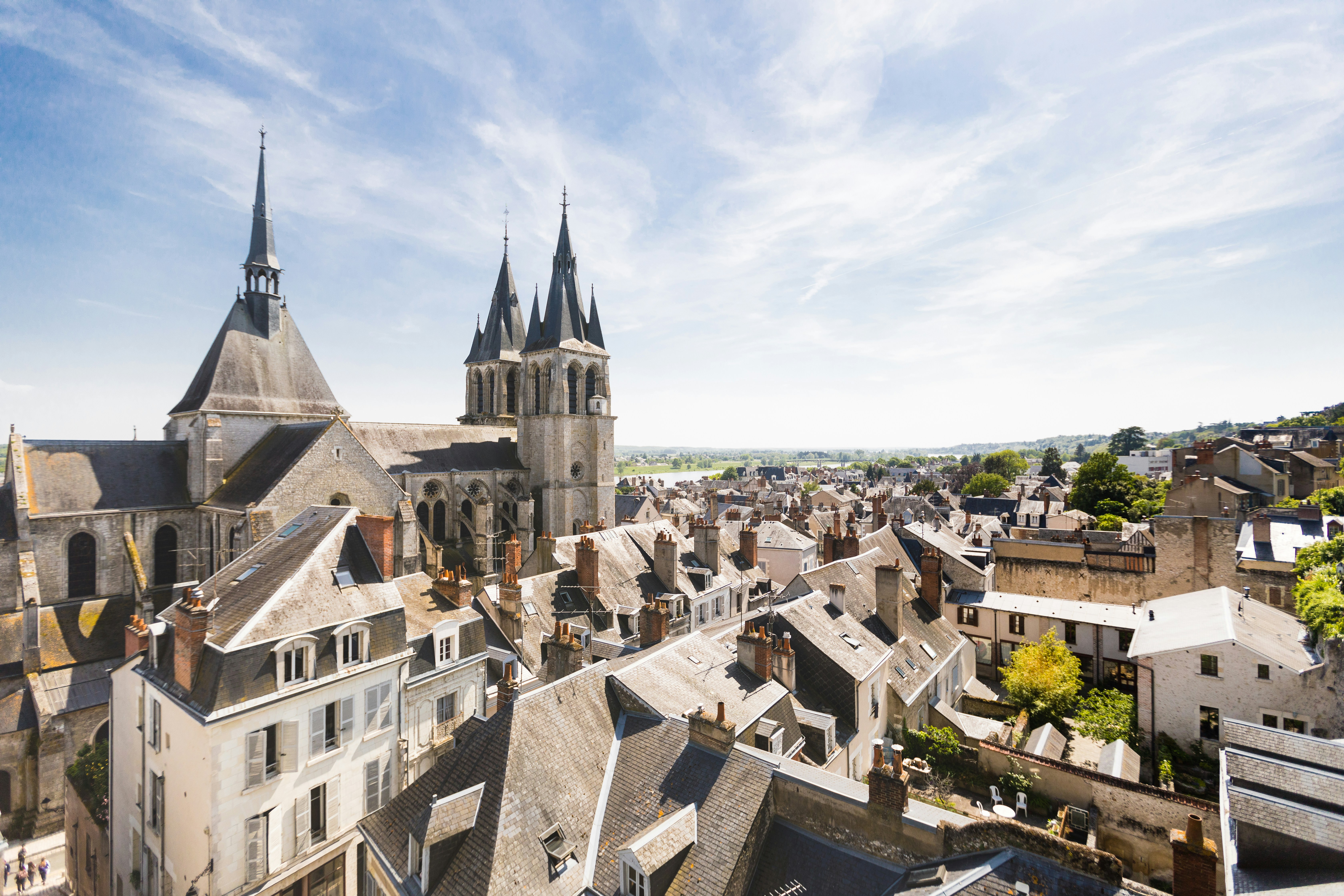Aerial view of a historic cathedral with towering spires surrounded by a quaint town under a bright blue sky.