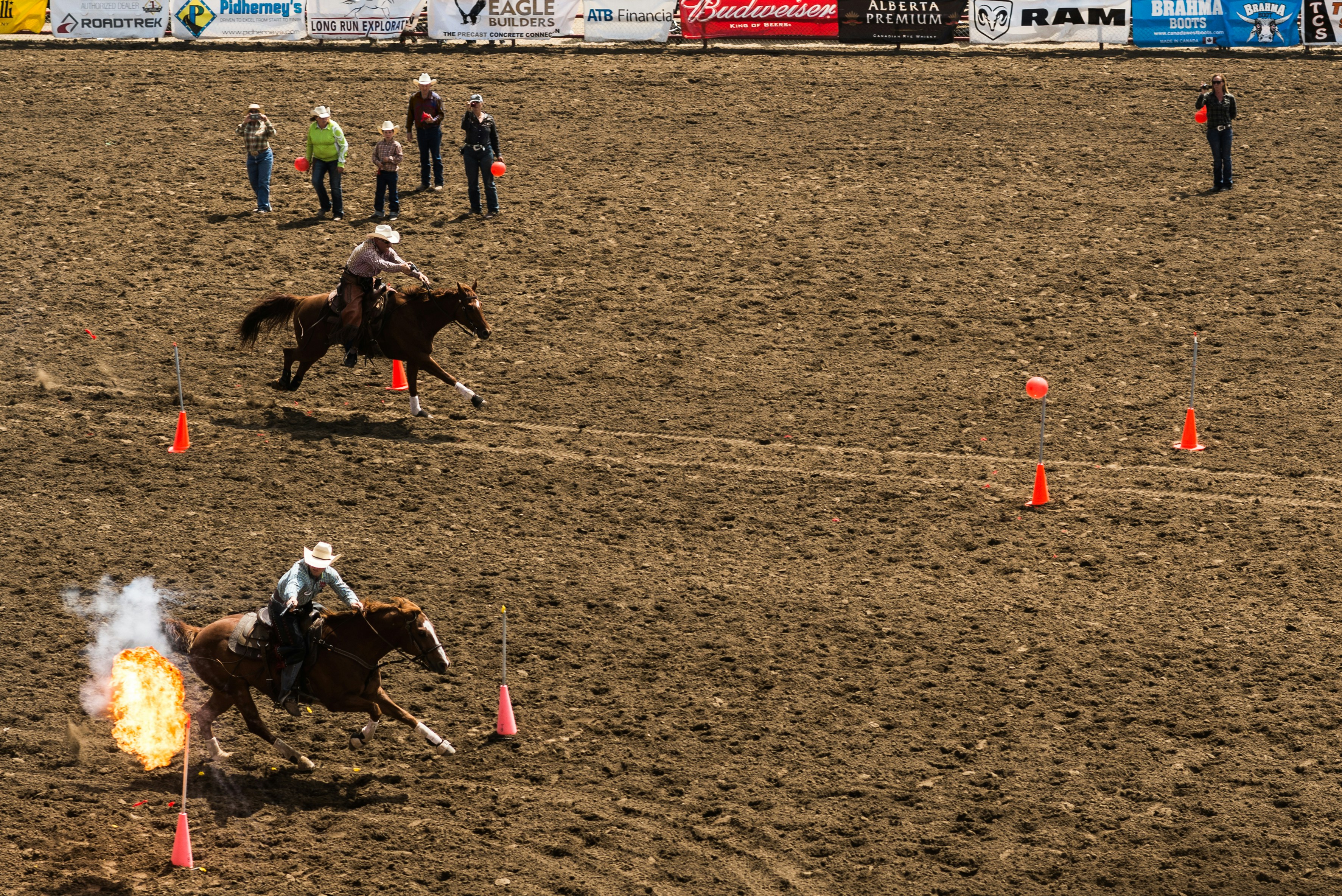 Riders on horseback compete in an arena, with one rider firing at targets creating a burst of flame.