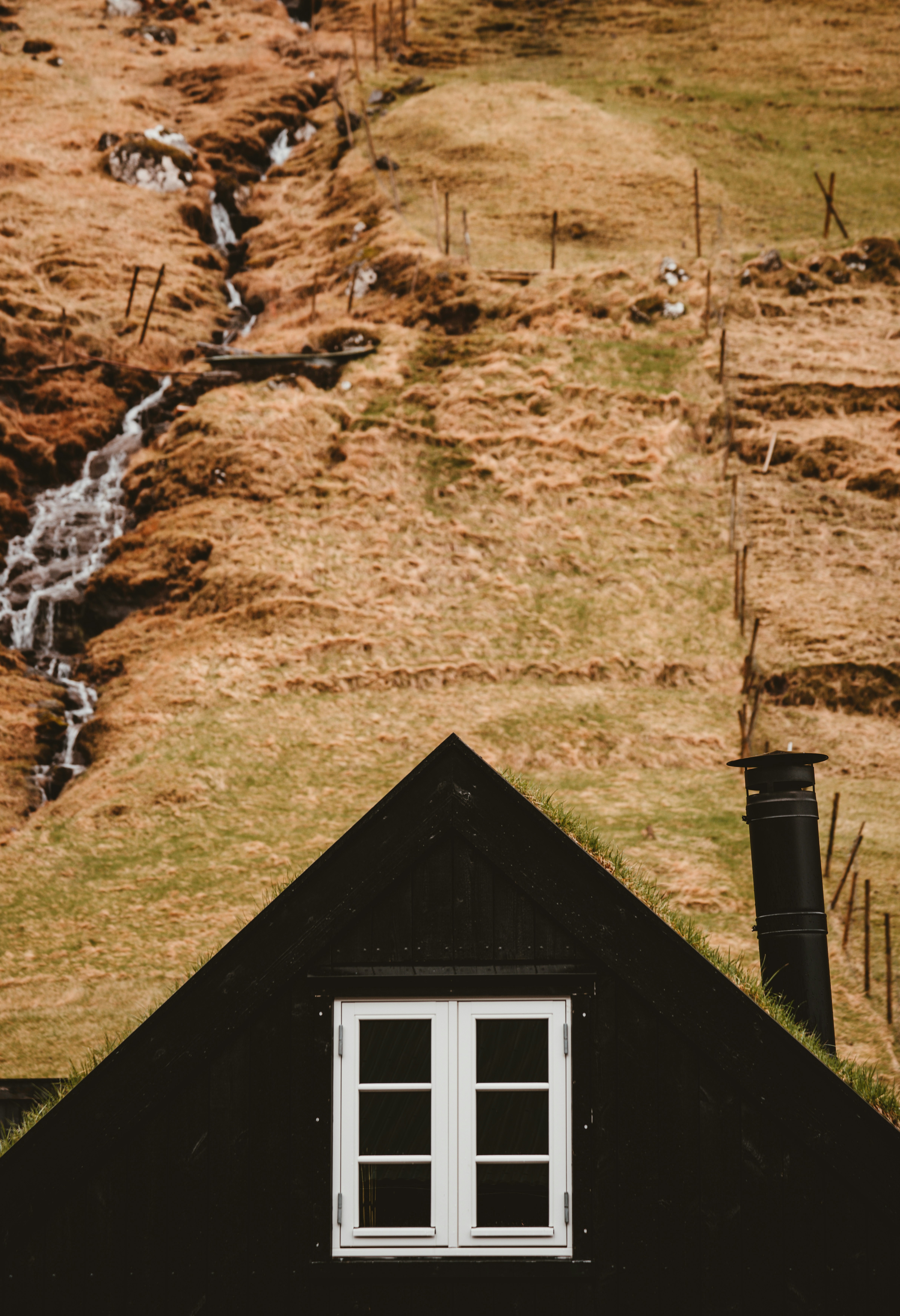 White-Frame Window on a Black Roof Beneath a Copper-Toned Hill