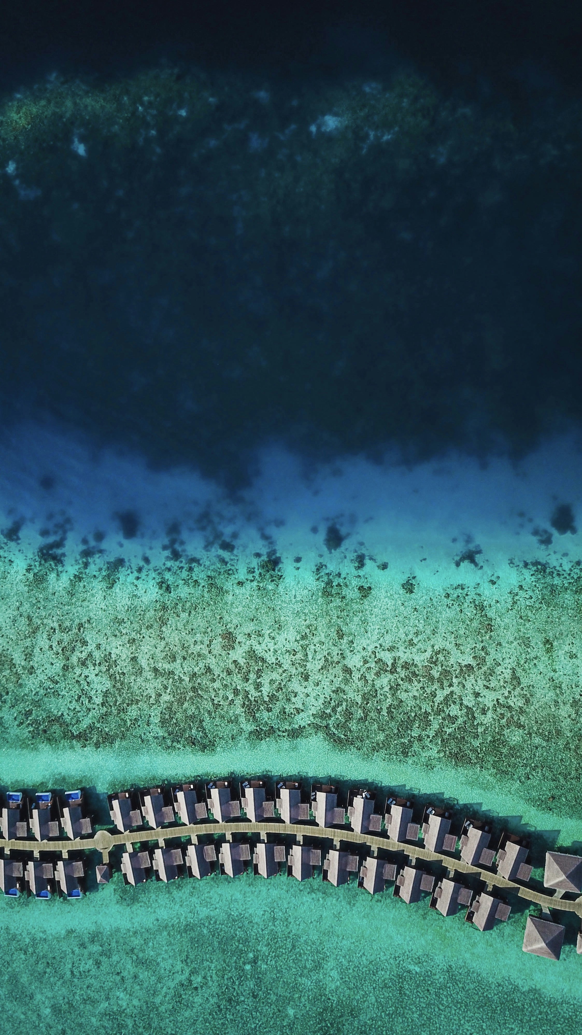 I was flying my drone on a resort in the Maldives when I saw the amazing visibility from above. The sea was crystal clear and you could literally see the reef slopes as in they are submerged from the water. This photo countains almost all the colors of ocean blues. | bird's-eye view photography of beach line