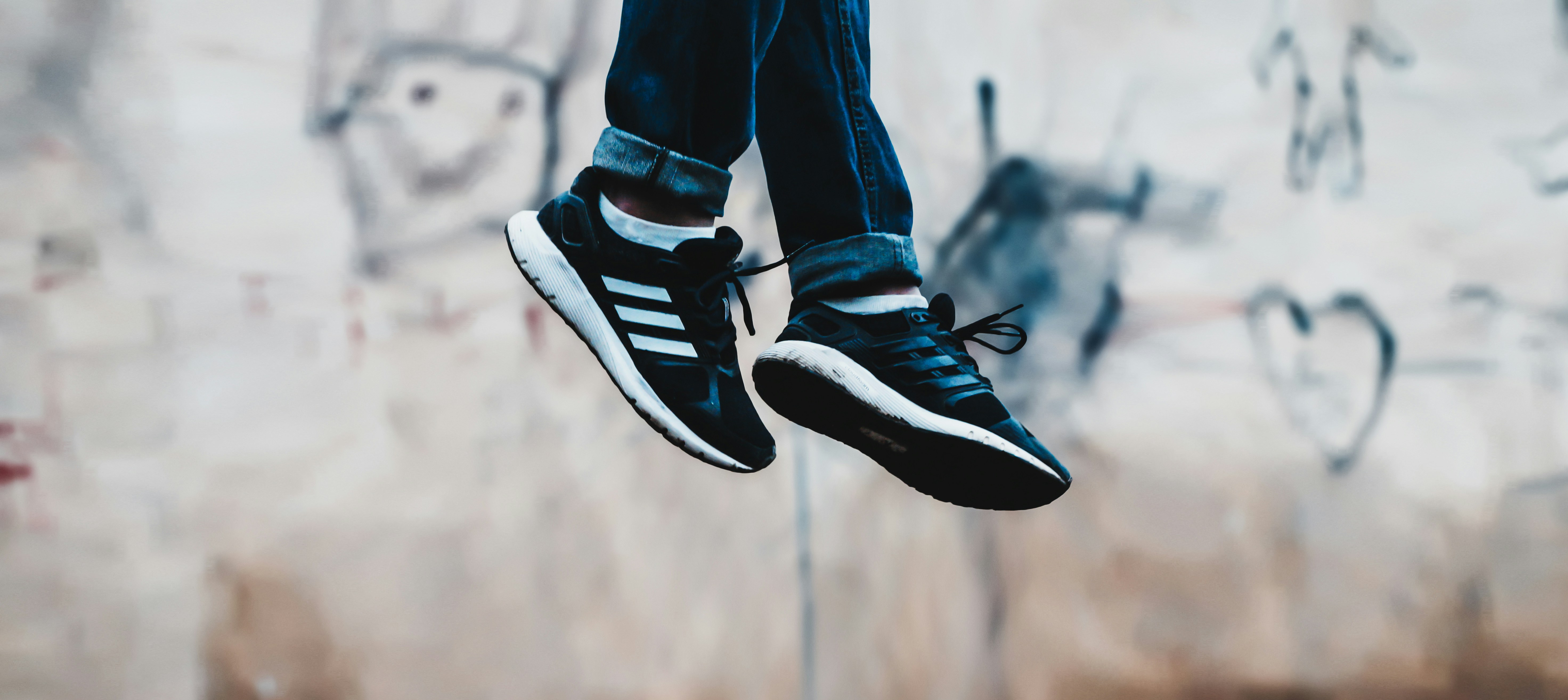 A pair of black and white athletic shoes suspended mid-air against a graffiti-covered wall, highlighting urban culture and style.