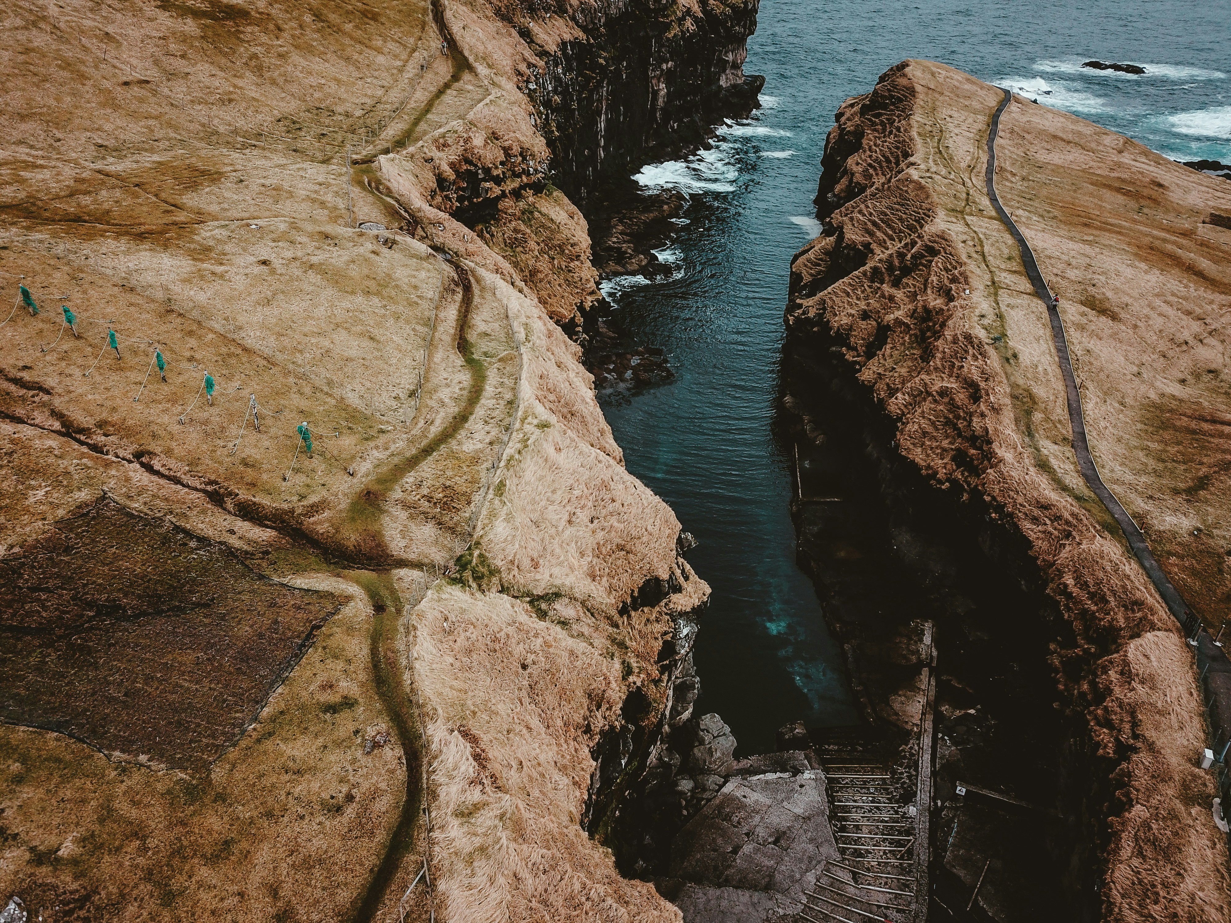 Aerial view of a narrow waterway flanked by rugged cliffs and winding paths, showcasing the stark beauty of the landscape. The scene captures the interplay of land and water.