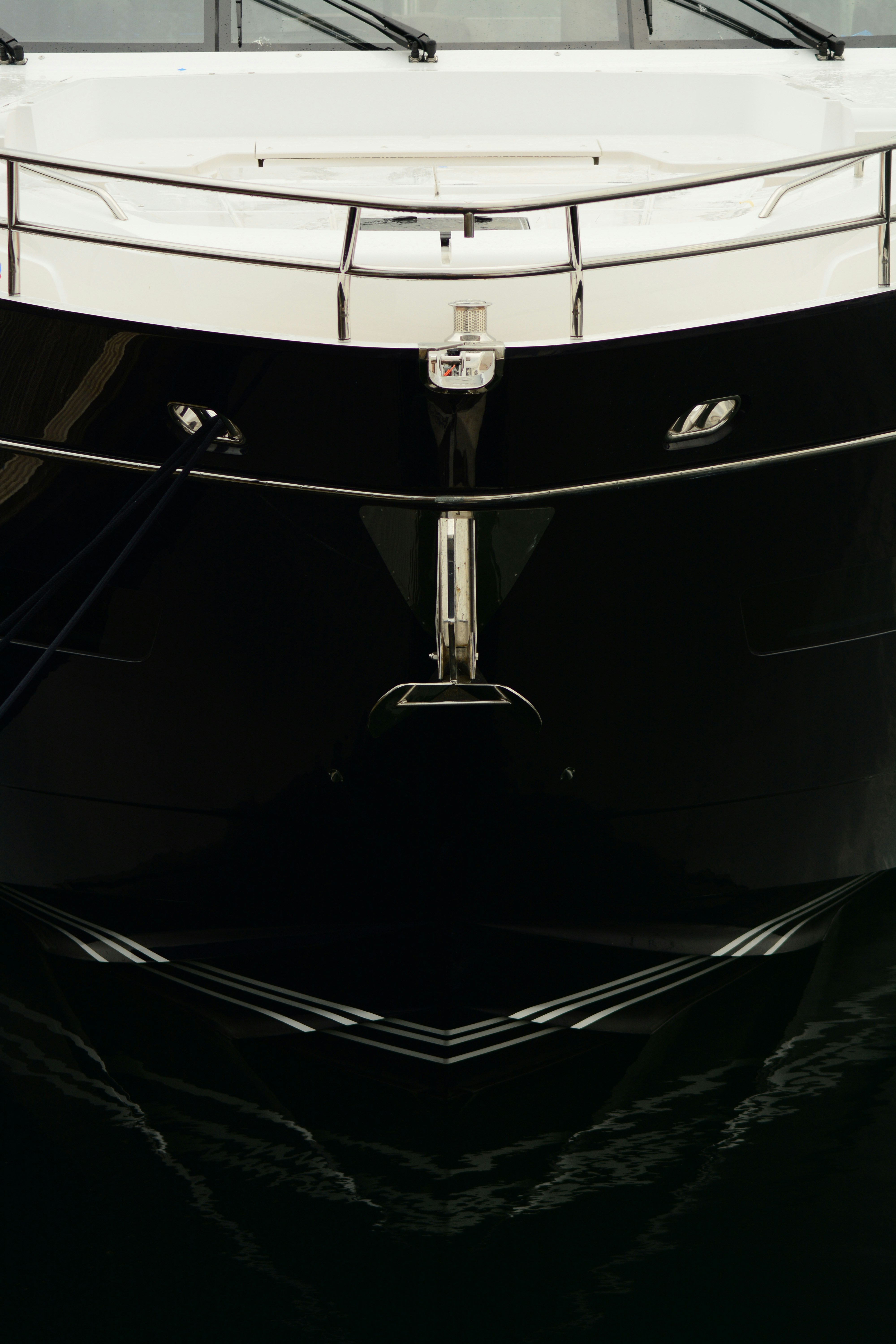 Sleek black yacht bow reflecting the surrounding water, showcasing elegant lines and design features.