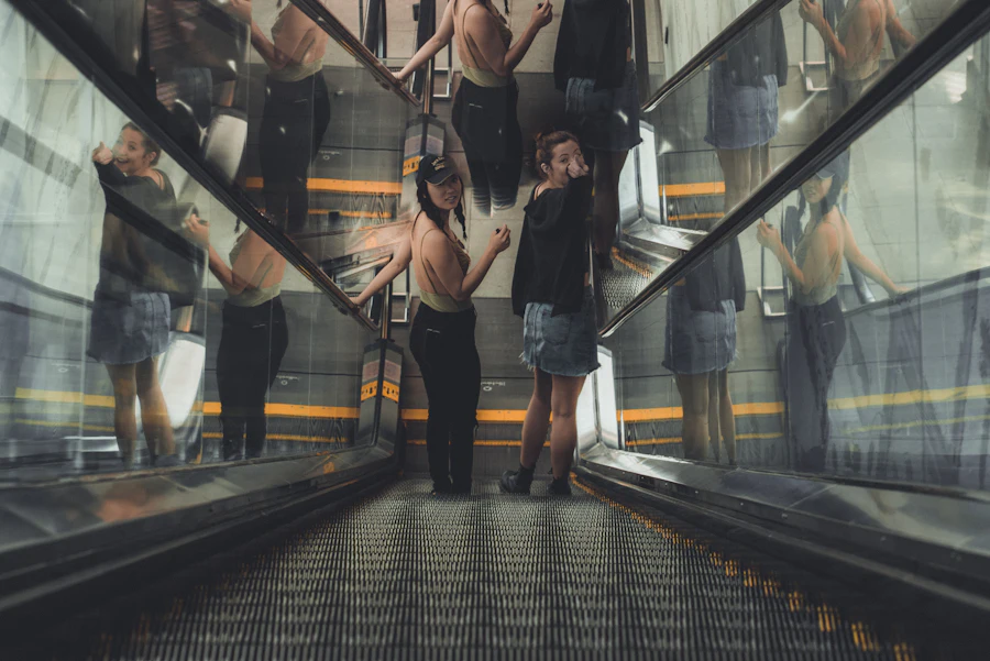 Two women stand on an escalator surrounded by mirrored glass and repeated reflections. Strong diagonal lines and layered reflections create a geometric, urban feel.
