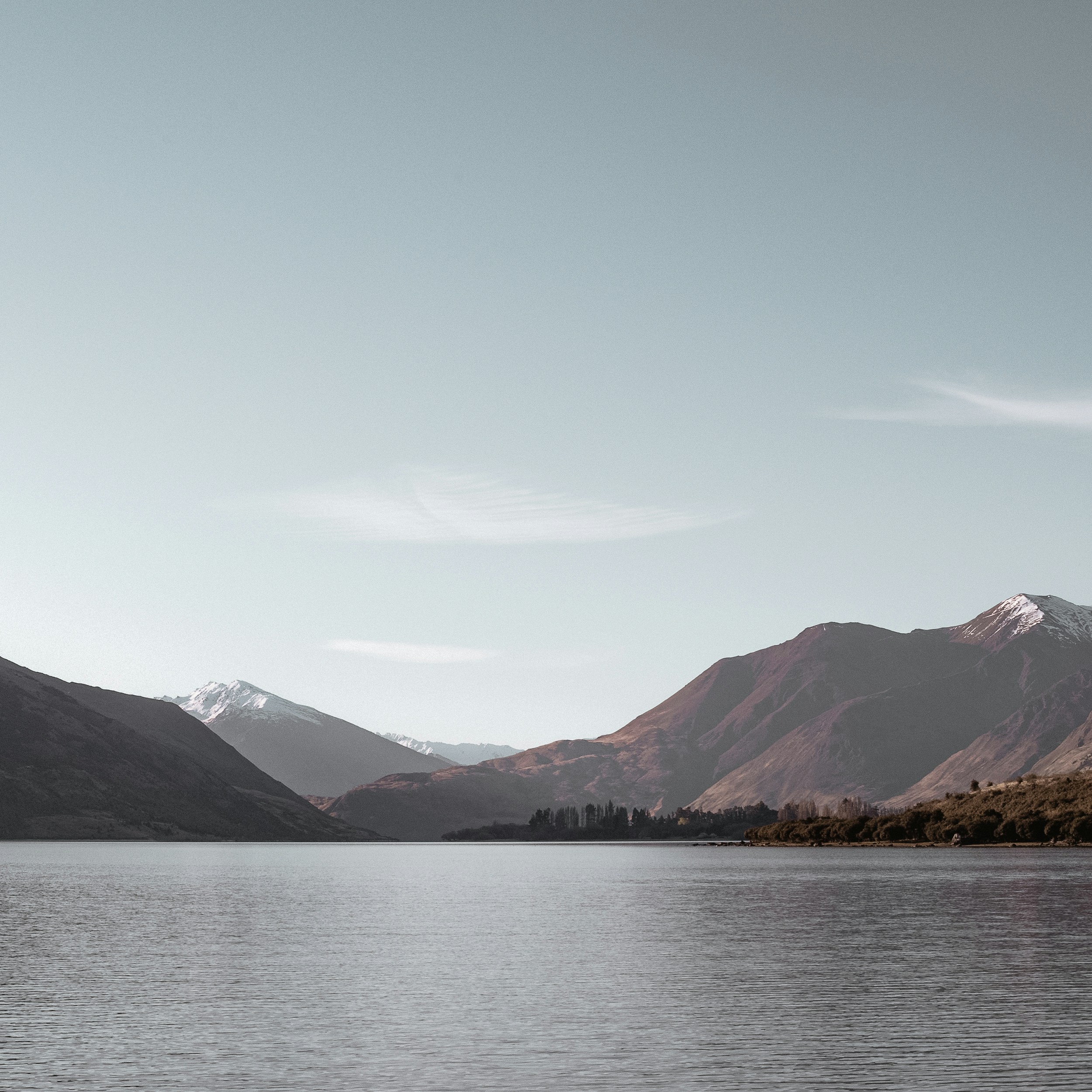 Gentle ripples on a serene lake reflect the soft hues of the sky, framed by distant mountains. The scene evokes a sense of calm and peacefulness.