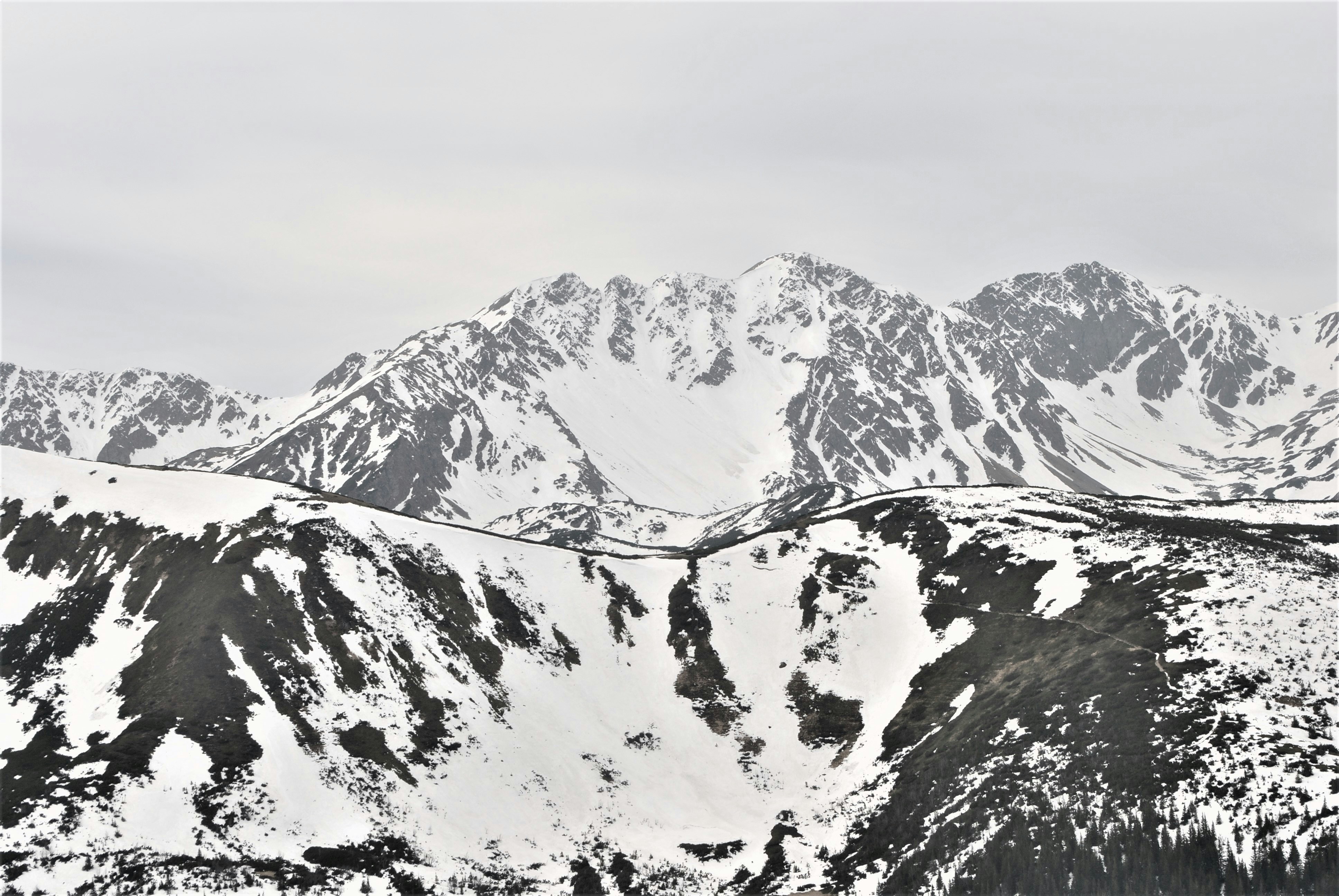 Snow-covered mountains rise majestically against a gray sky, showcasing rugged terrain and serene beauty.