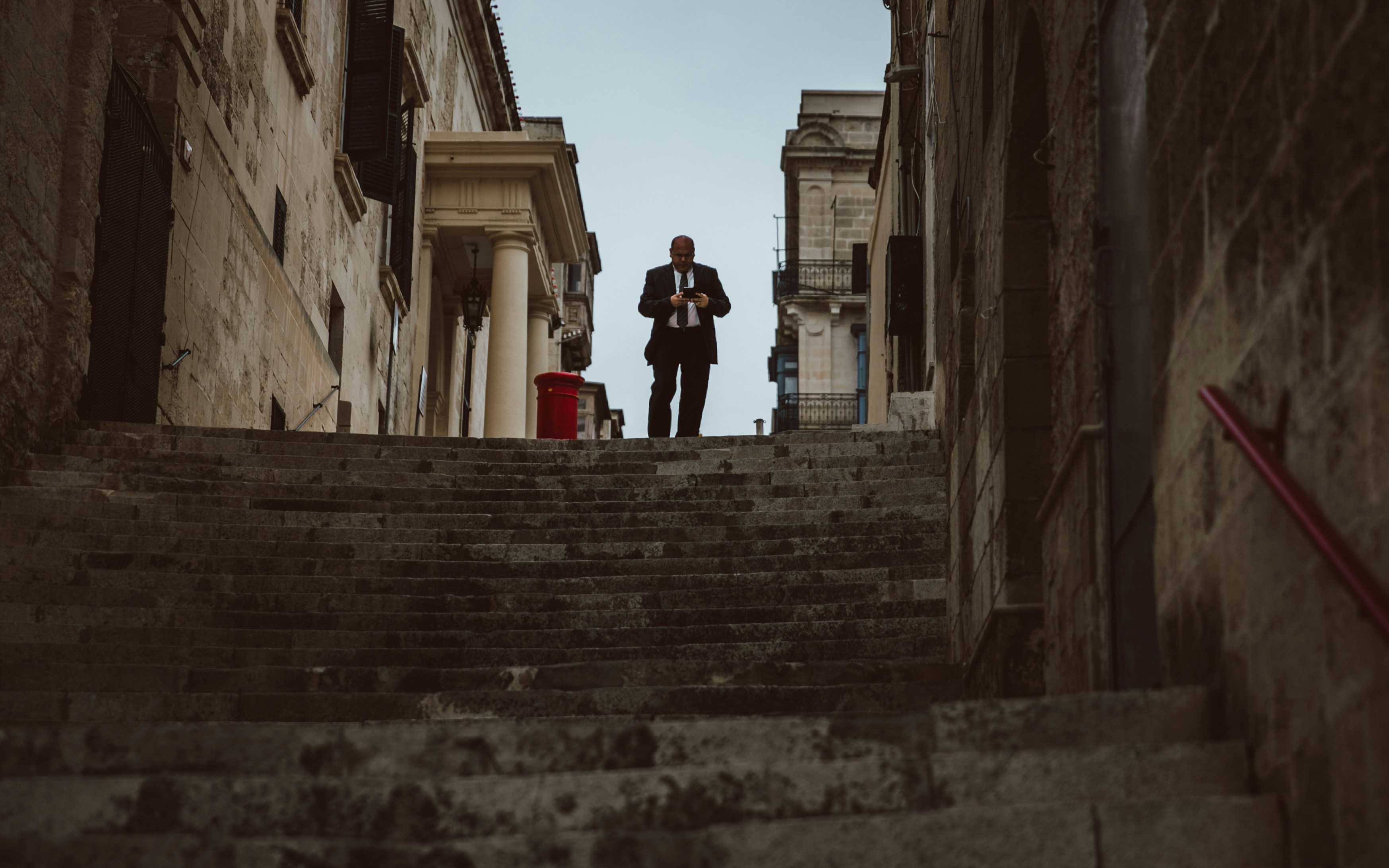 Businessman ascending weathered stone steps flanked by historic buildings, evoking a sense of journey and purpose.