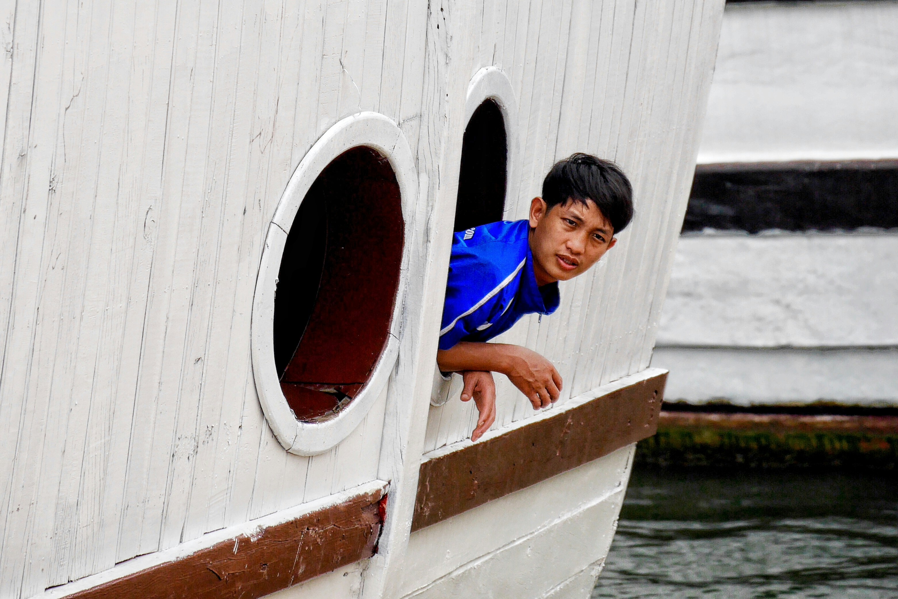 Young boy in a blue shirt peering out from a boat's porthole in Ha Long Bay.