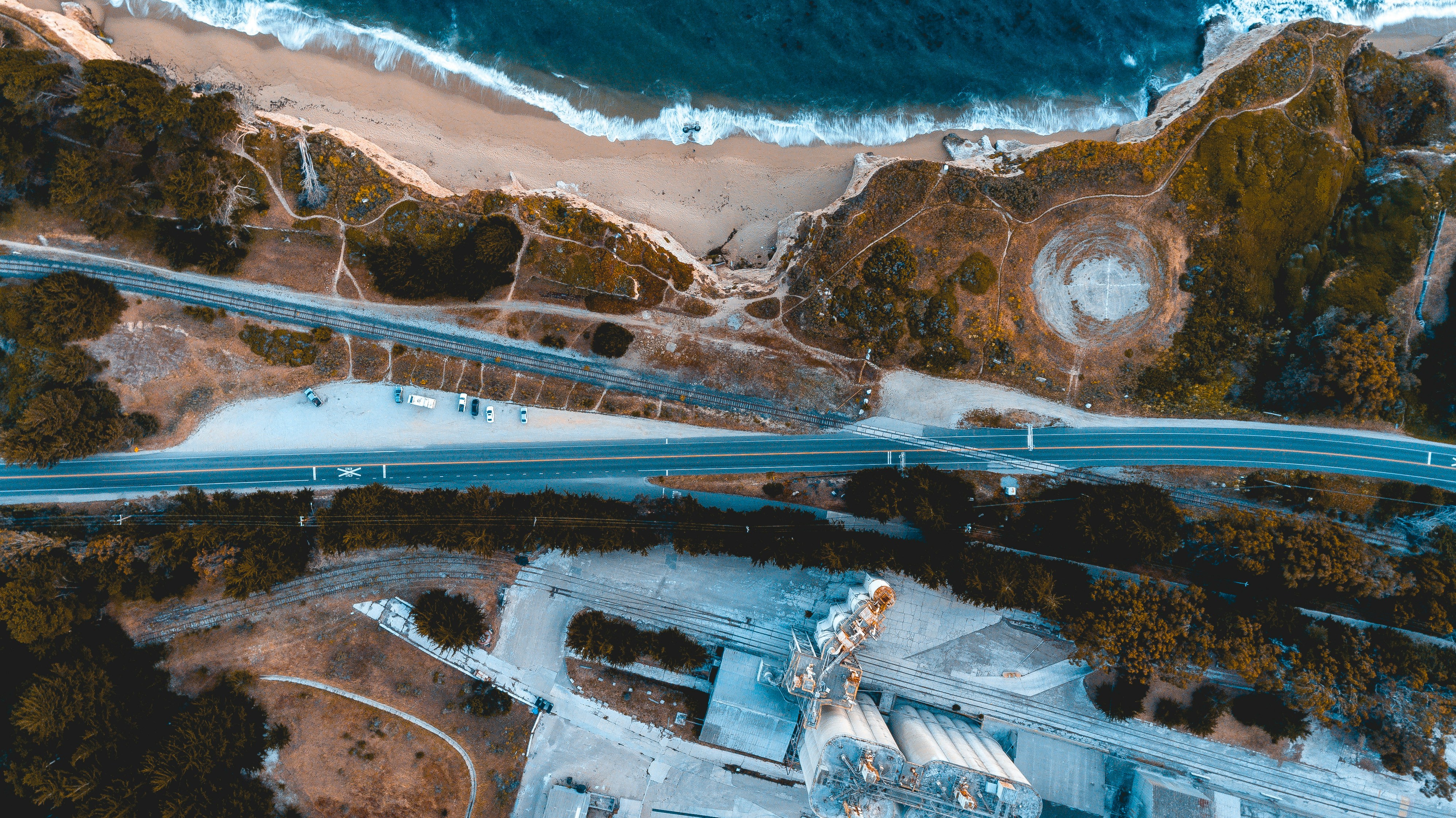 Aerial view of a winding coastal road meeting the ocean, surrounded by lush greenery and sandy beaches.